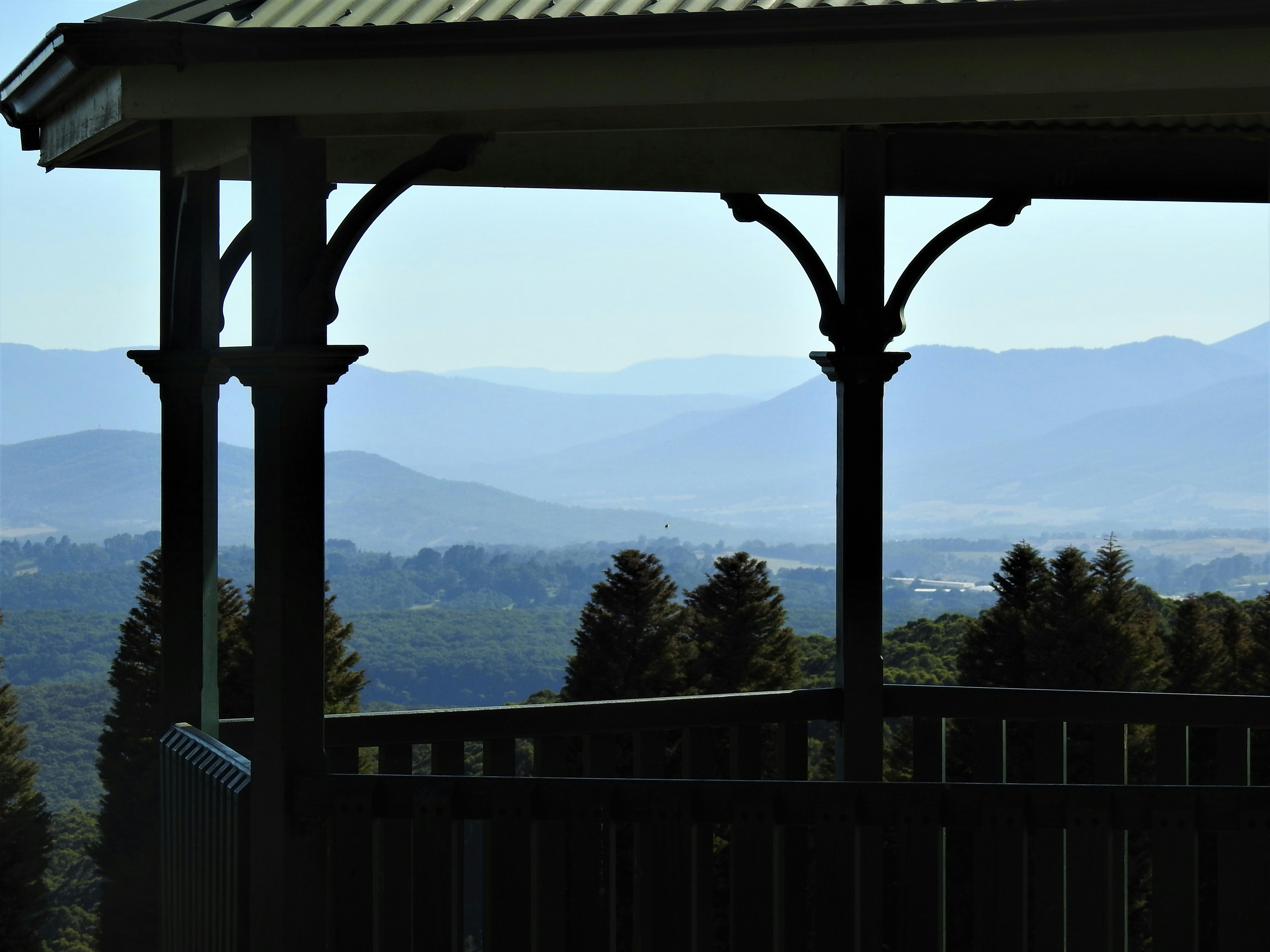 A wooden gazebo frames distant blue mountains under a clear sky.