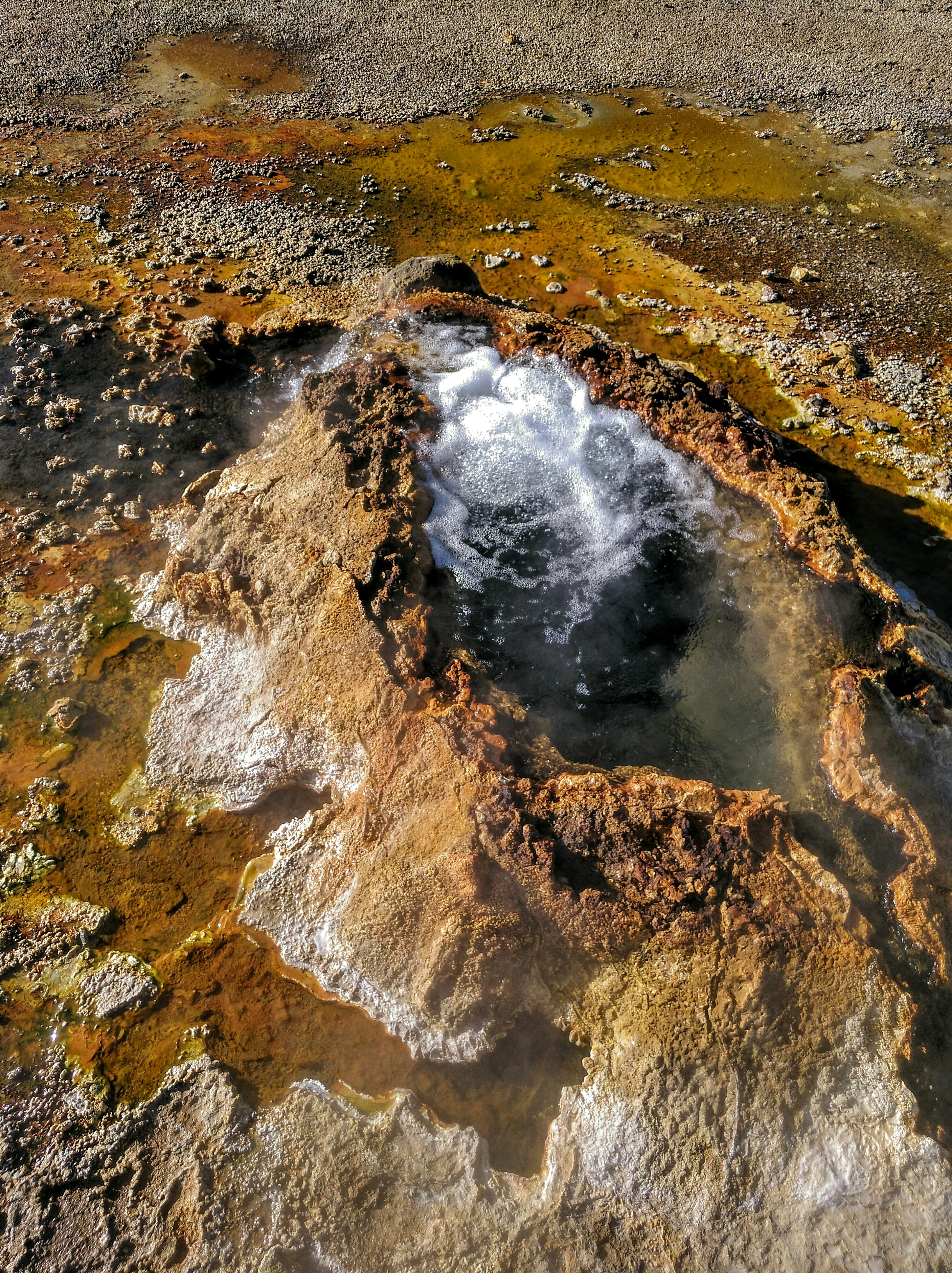 Steaming geothermal spring surrounded by vivid mineral deposits in earthy hues.