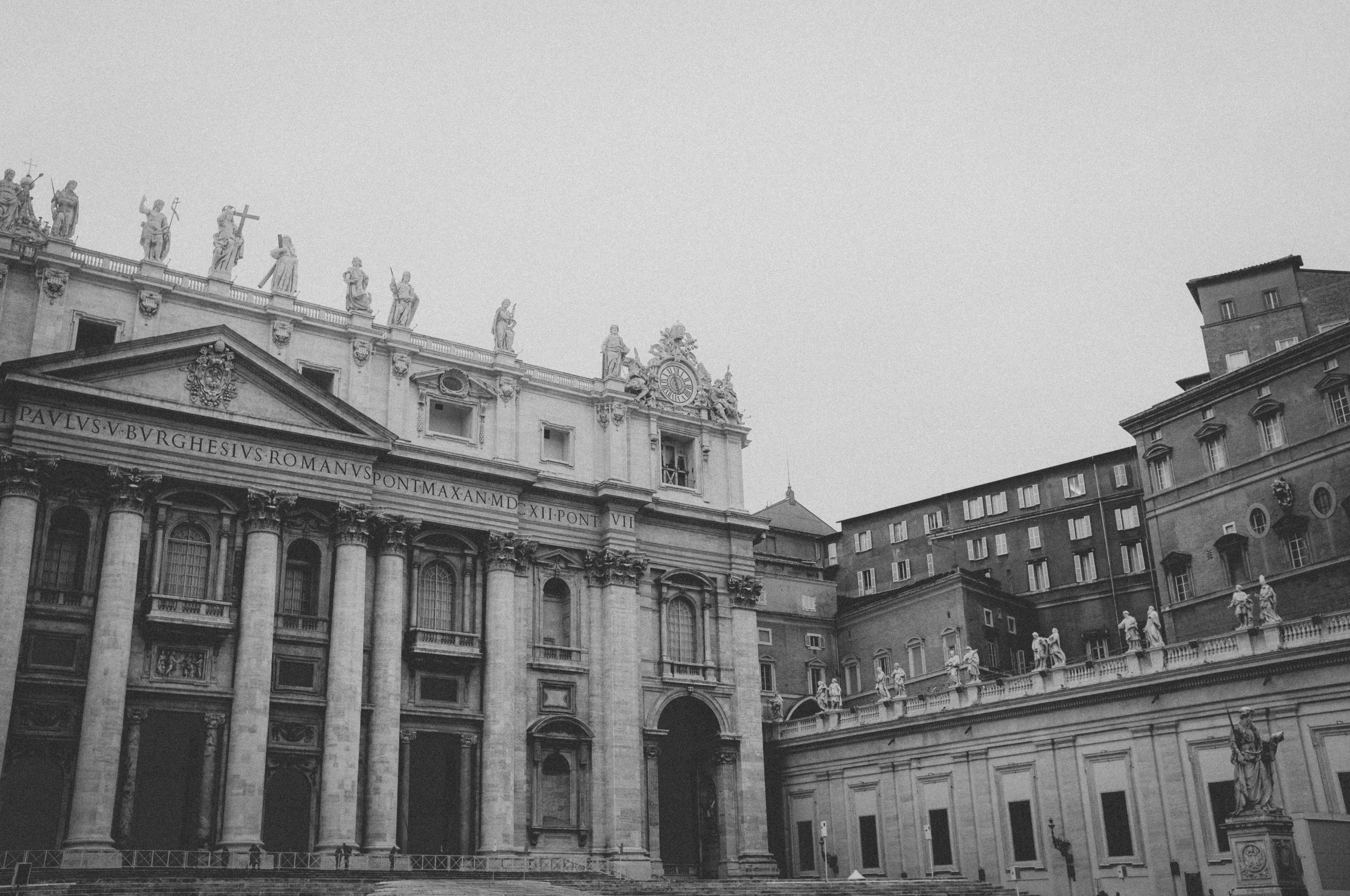 Majestic architecture of Vatican City, showcasing intricate details of the façade and statues against a cloudy sky.