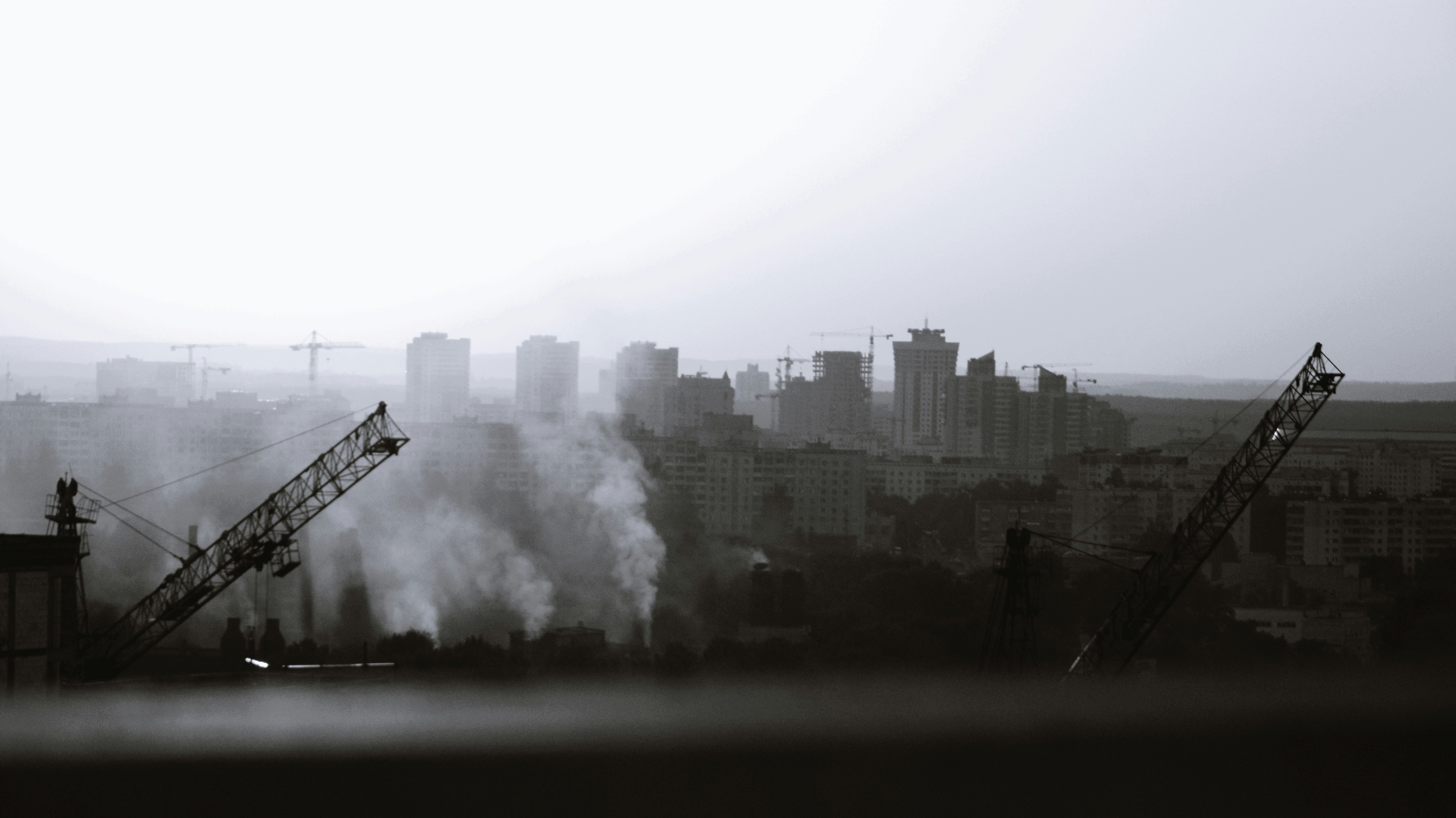 Crane Silhouettes Over a Smoke-Hazed City Horizon