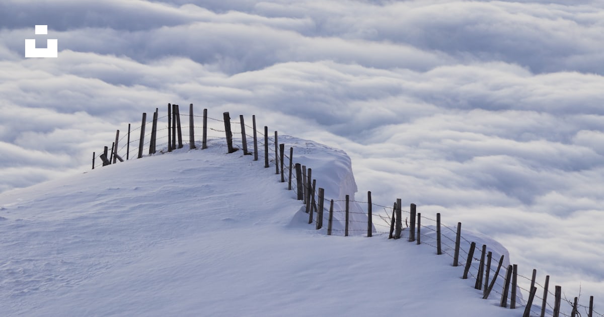 昼間は白い雲と青空の下、雪に覆われた地面に茶色の木製の柵の写真 Unsplashのスイスの無料画像