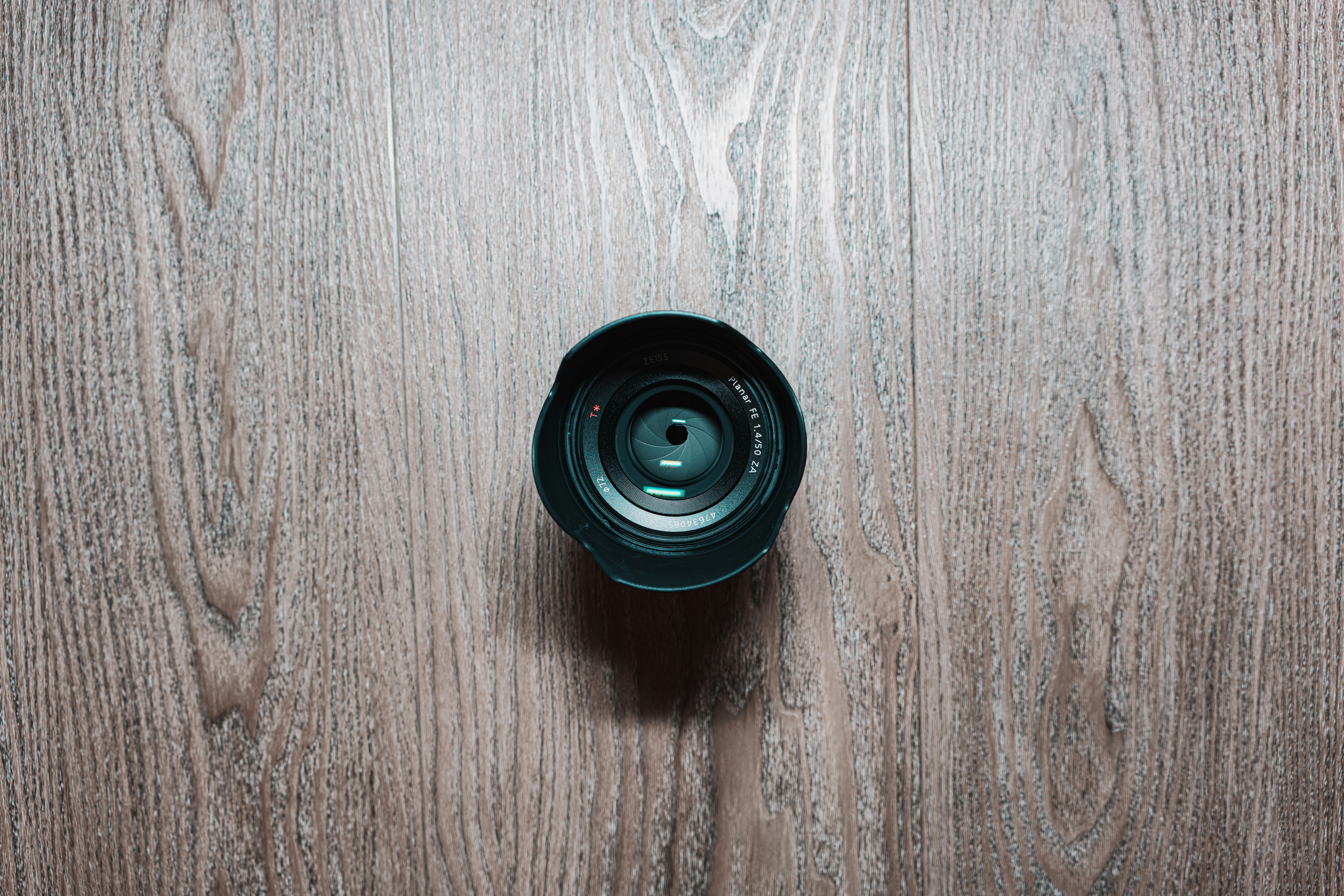 Camera lens positioned centrally on a textured wooden surface, highlighting its intricate design and craftsmanship.