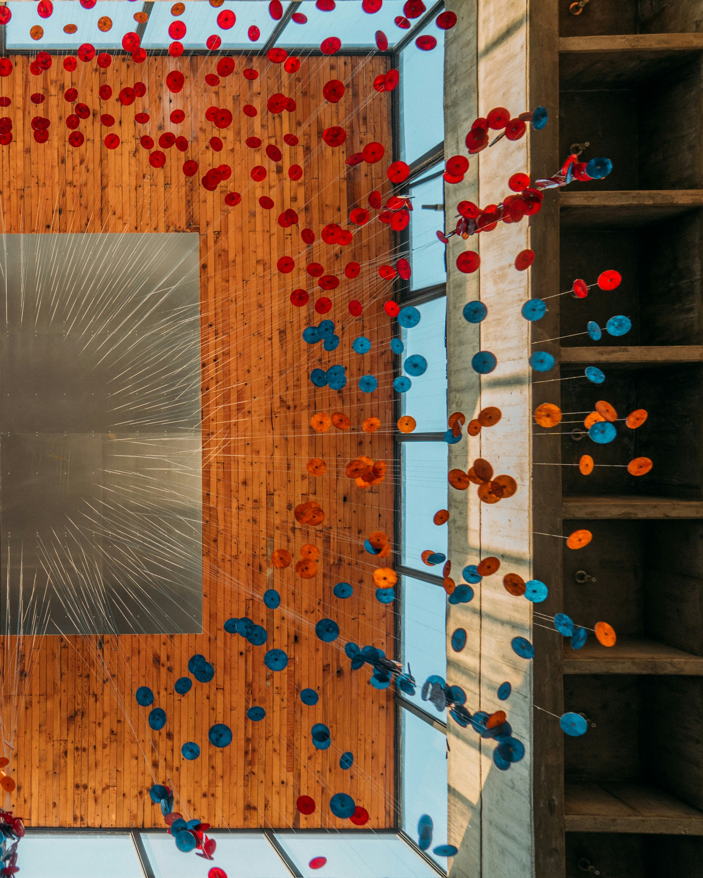 Suspended Color Discs Cascading Through a Wooden Atrium