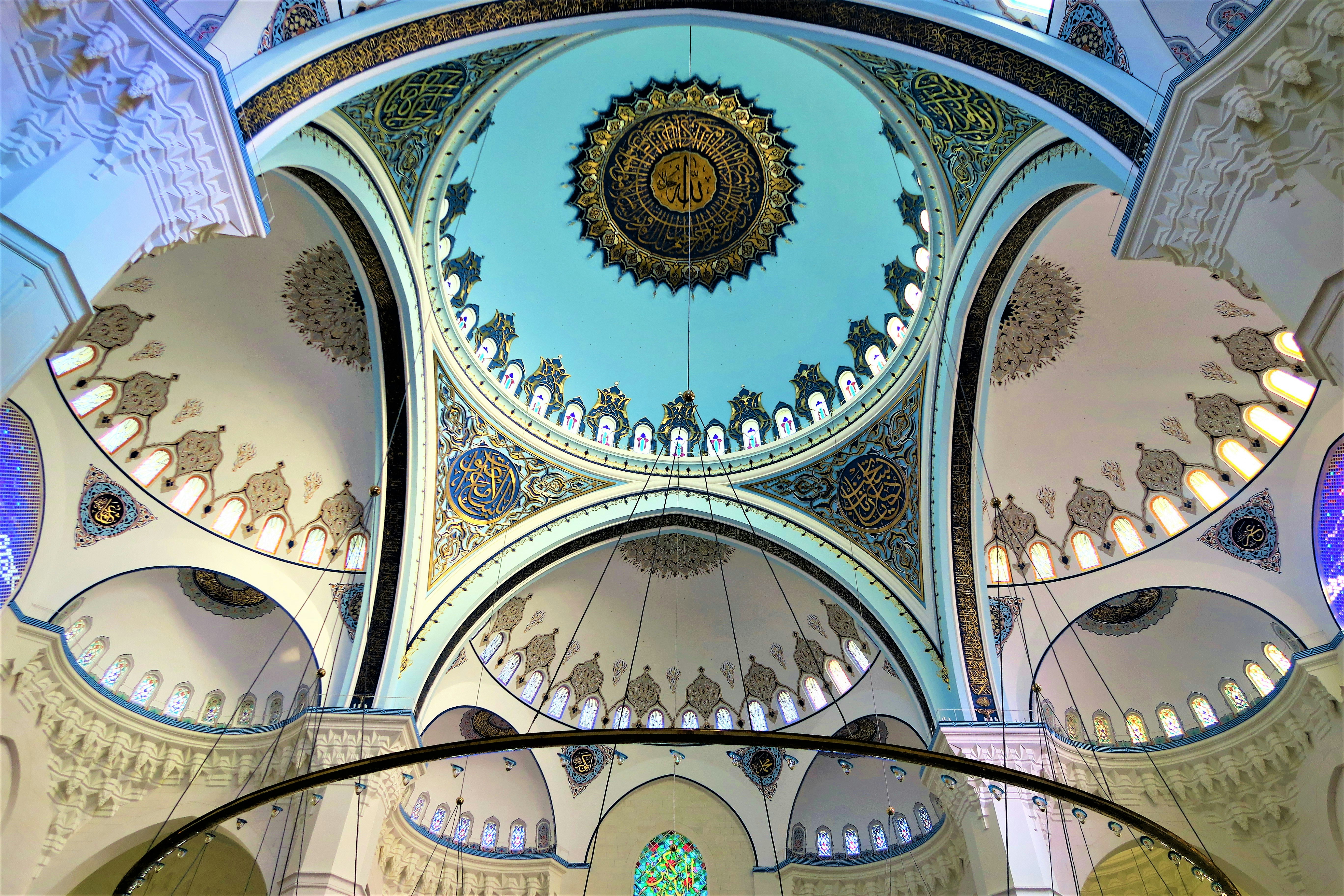 Intricate dome adorned with ornate designs and vibrant stained glass in a grand mosque interior.