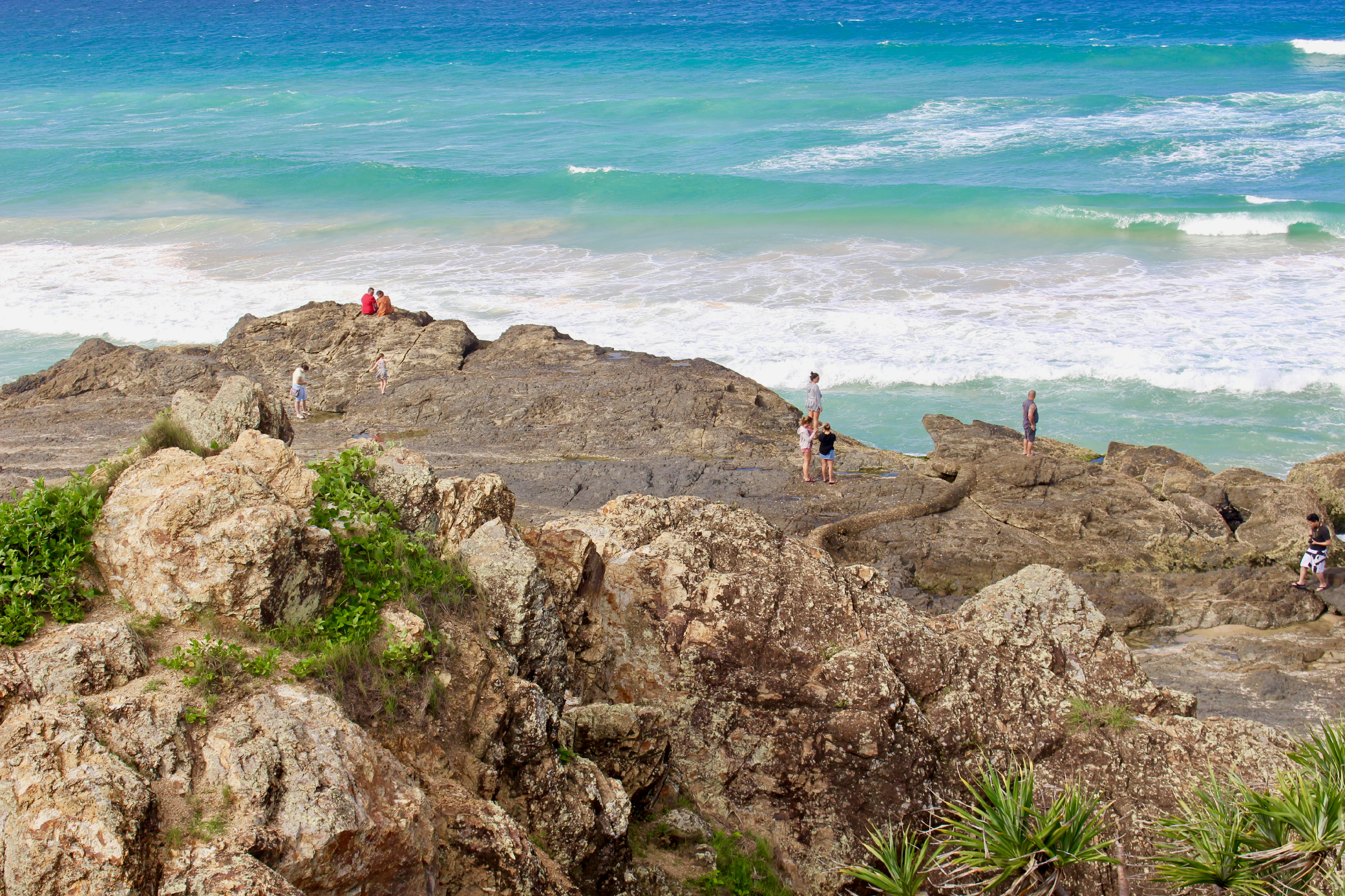 Rugged Rocks Meet the Sea: People exploring a sunlit coastal outcrop