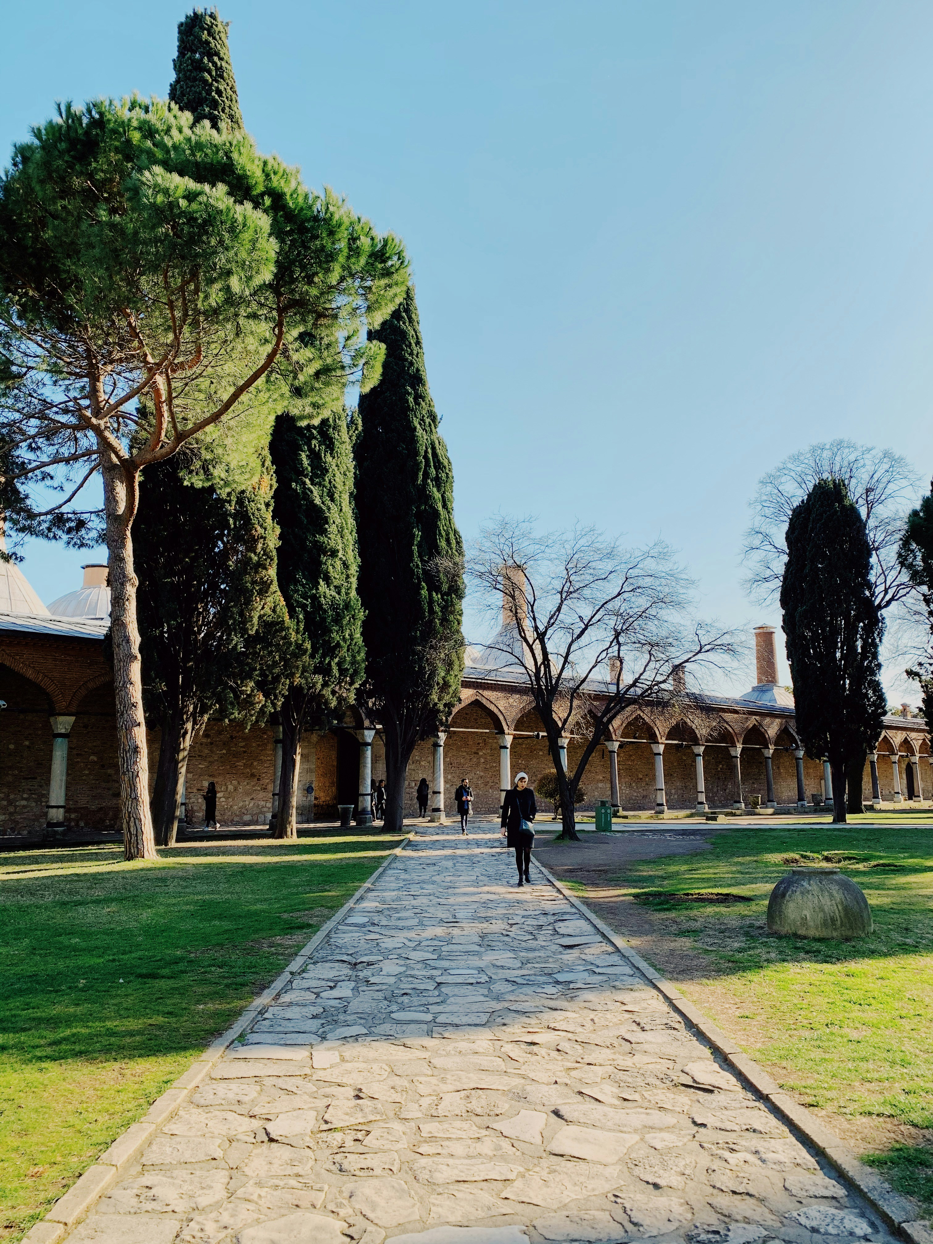 A serene pathway lined with towering cypress trees leads to an ancient stone structure, inviting exploration and reflection.