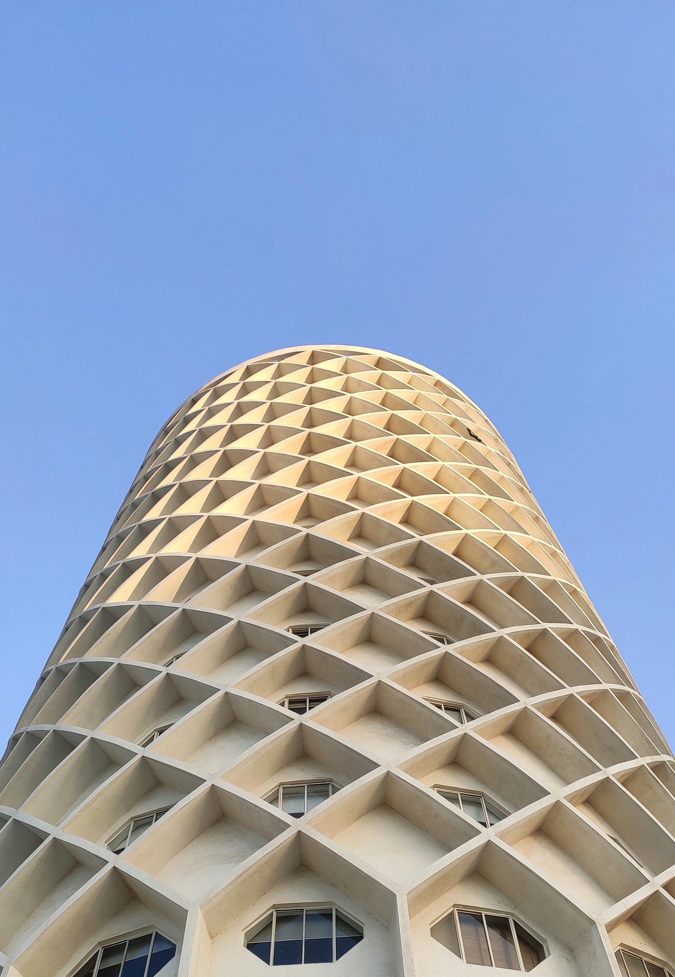 A cylindrical building featuring a striking geometric façade, showcasing a pattern of hexagonal shapes against a clear blue sky.