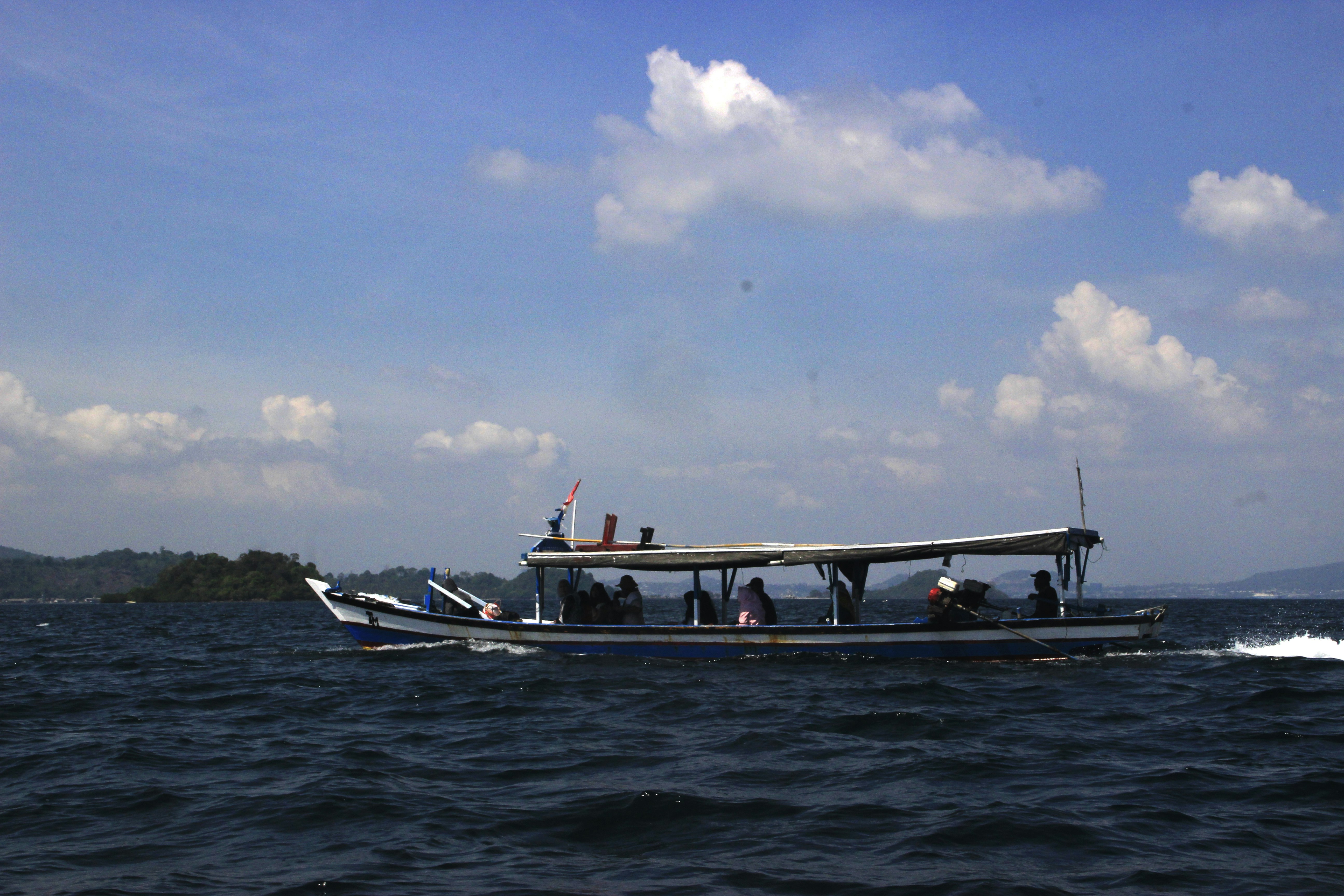 A traditional boat glides across calm waters under a blue sky dotted with fluffy clouds.