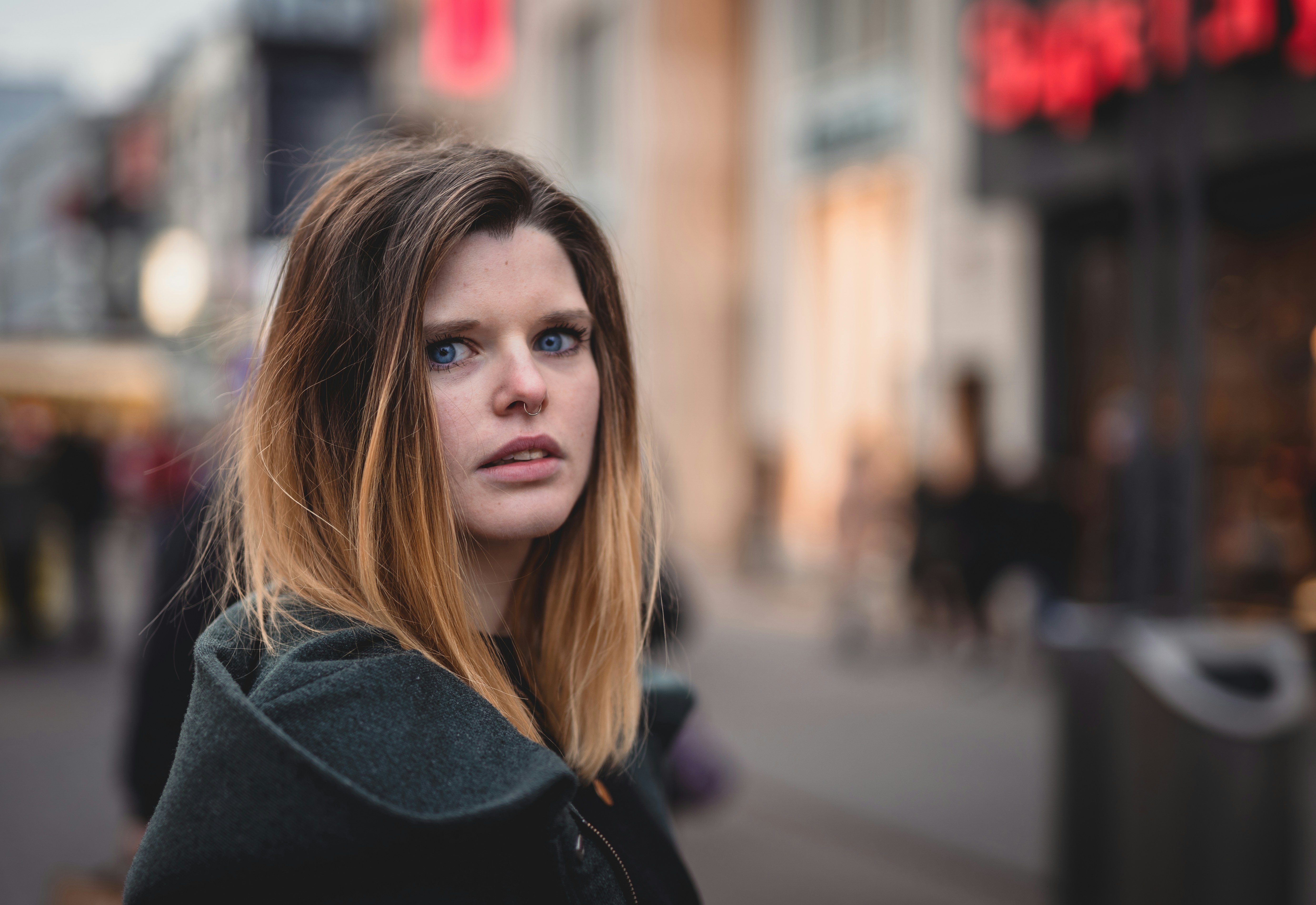 Woman with blue eyes in a city street, looking directly at the camera amidst a blurred background.