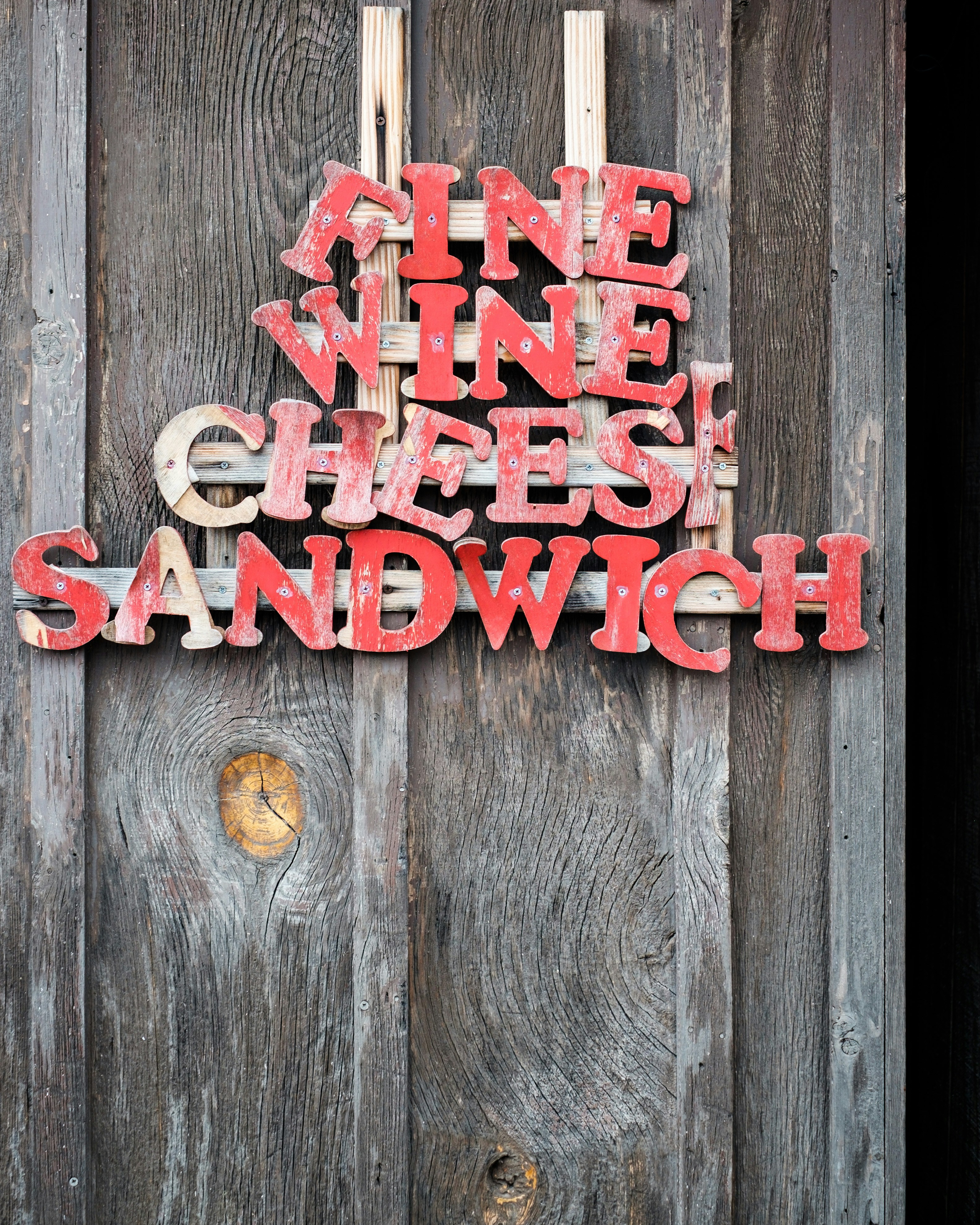 Colorful wooden letters spell out 'FINE WINE CHEESE SANDWICH' on a rustic wooden backdrop, inviting culinary exploration.