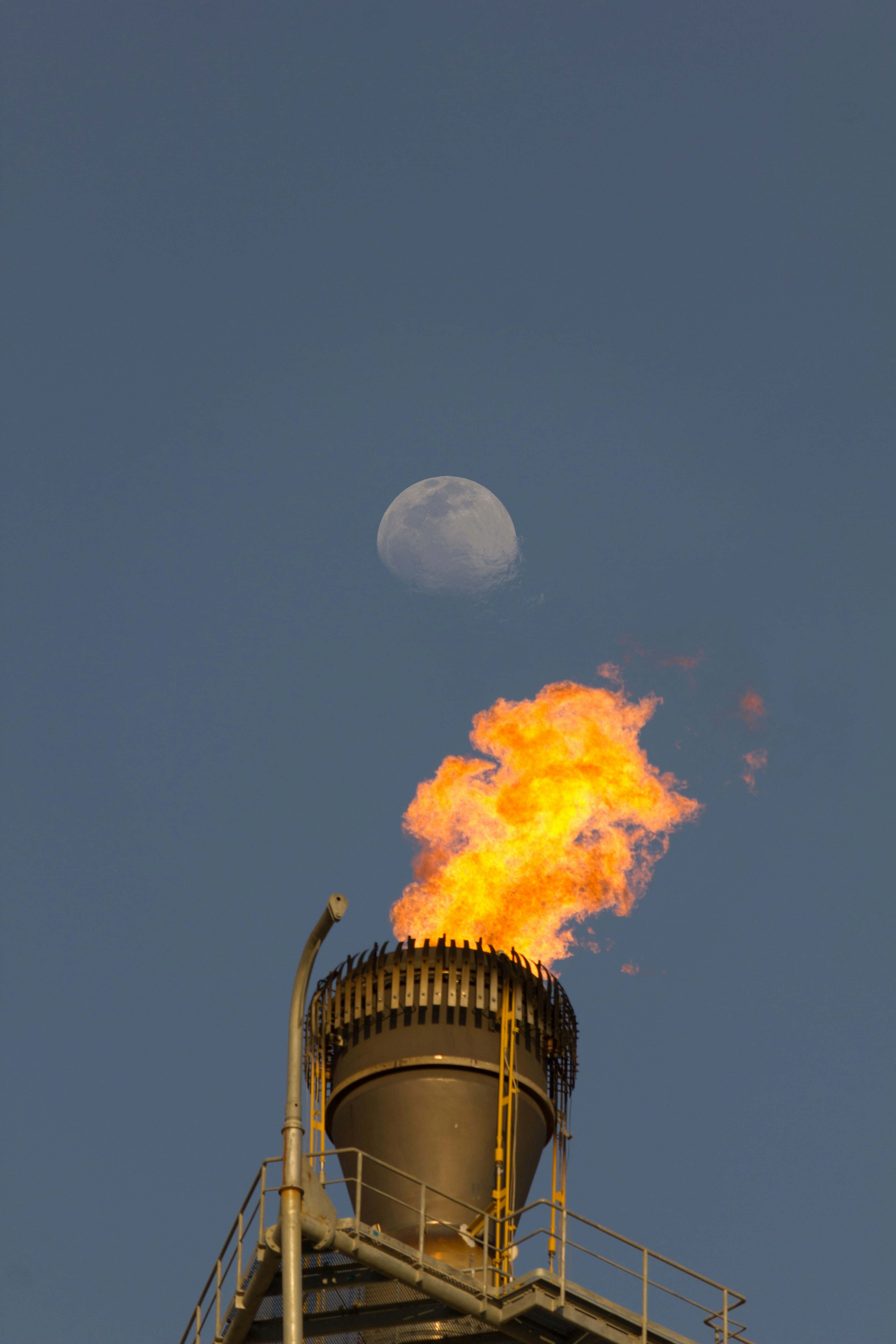 Daylight Inferno Over a Flare Stack Under a Moonlit Sky