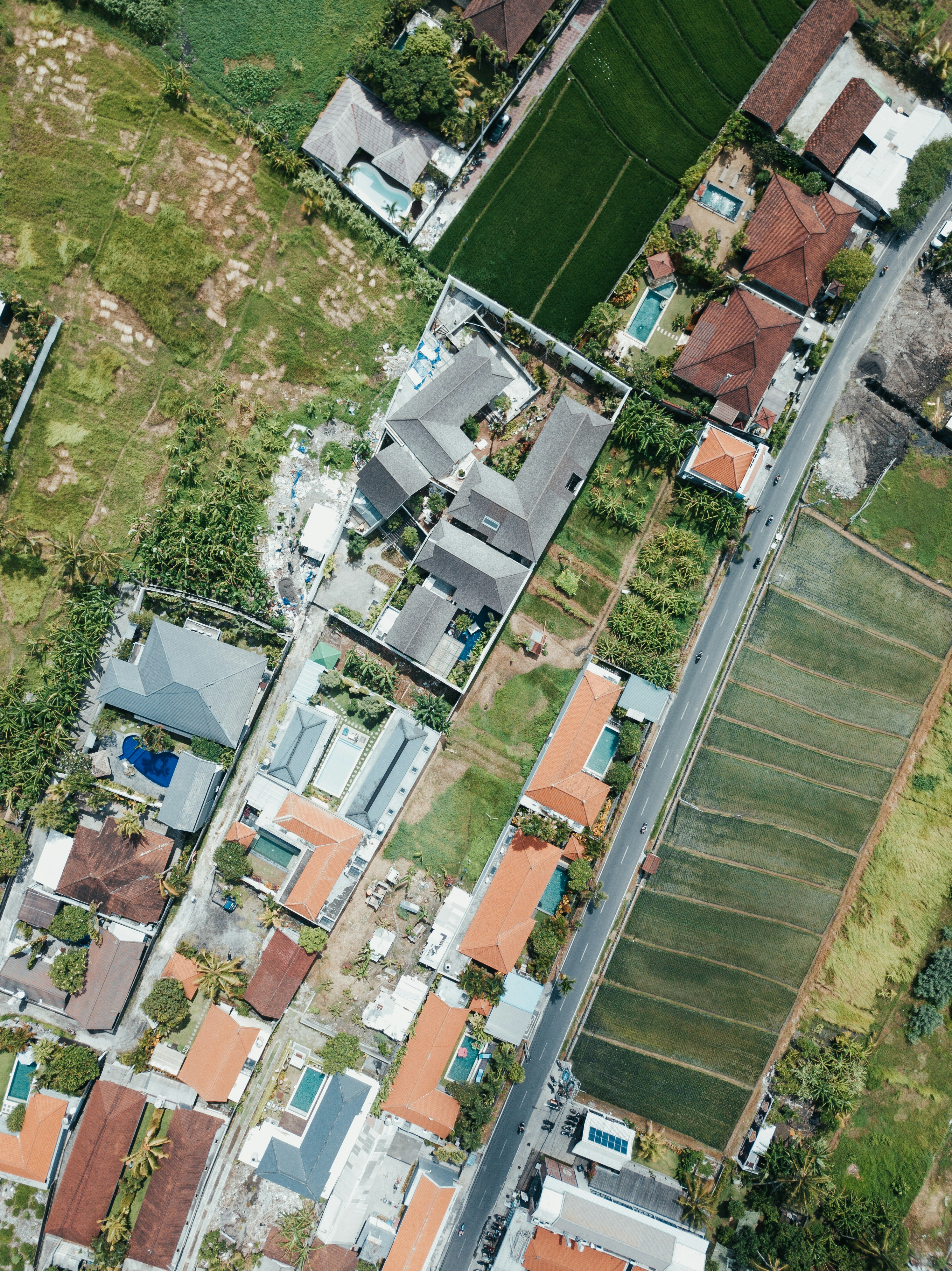 Aerial view showcasing a blend of residential areas, agricultural fields, and a winding road, illustrating the coexistence of urban and rural landscapes.