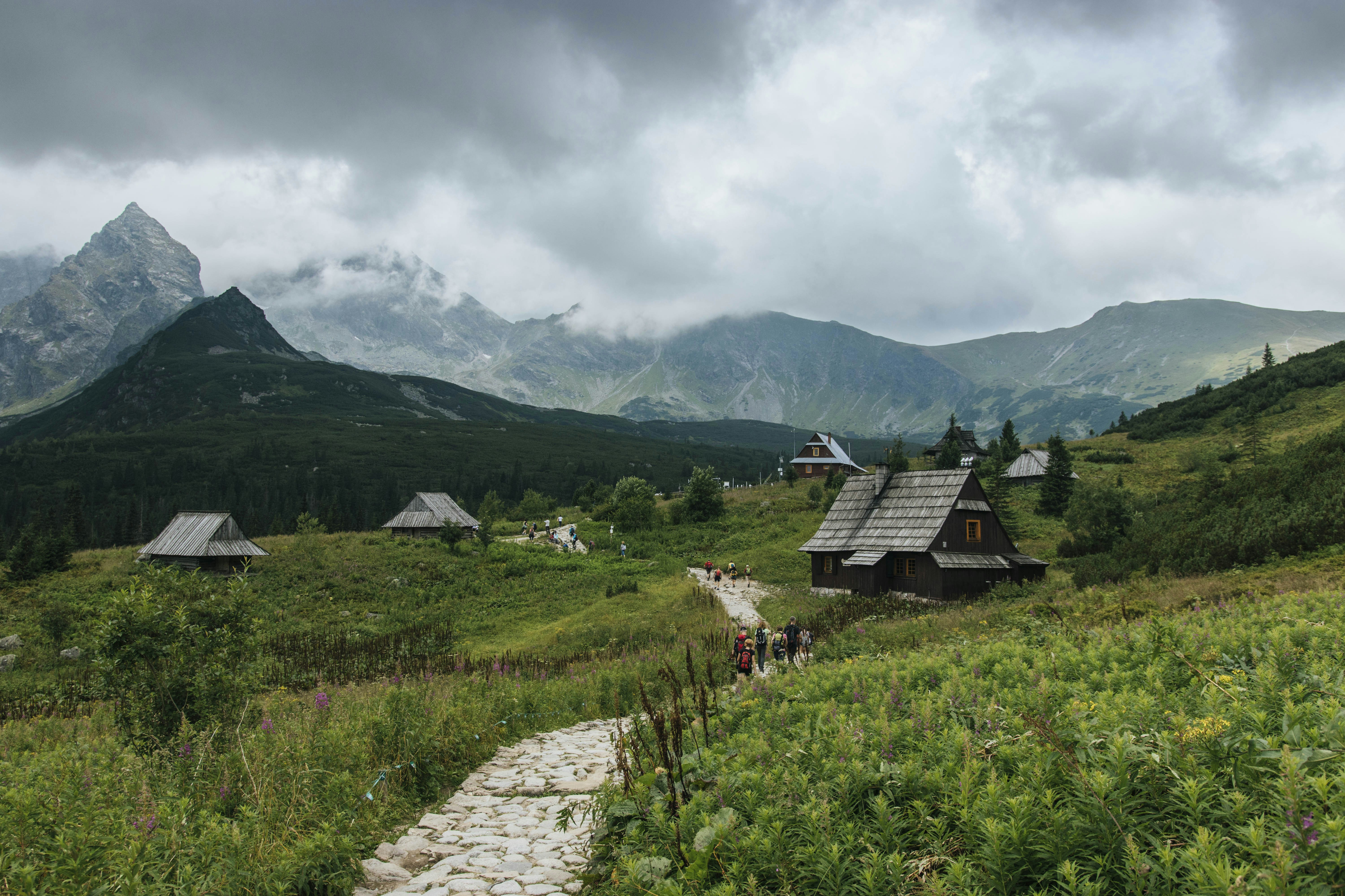 brown wooden house on green grass field near mountain under white clouds during daytime