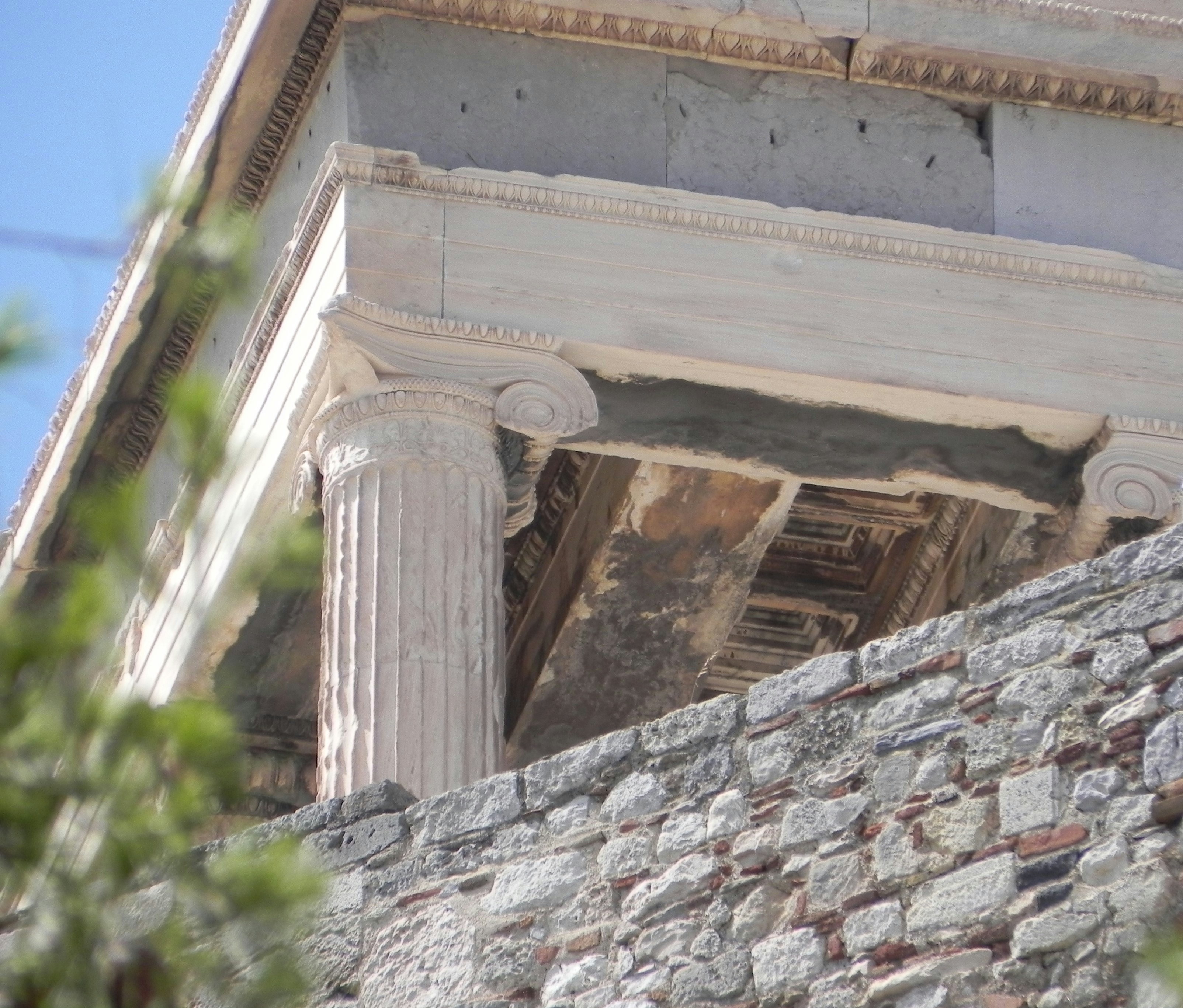 Close-up of a weathered column supporting a historic structure, showcasing intricate details against a backdrop of stone masonry.
