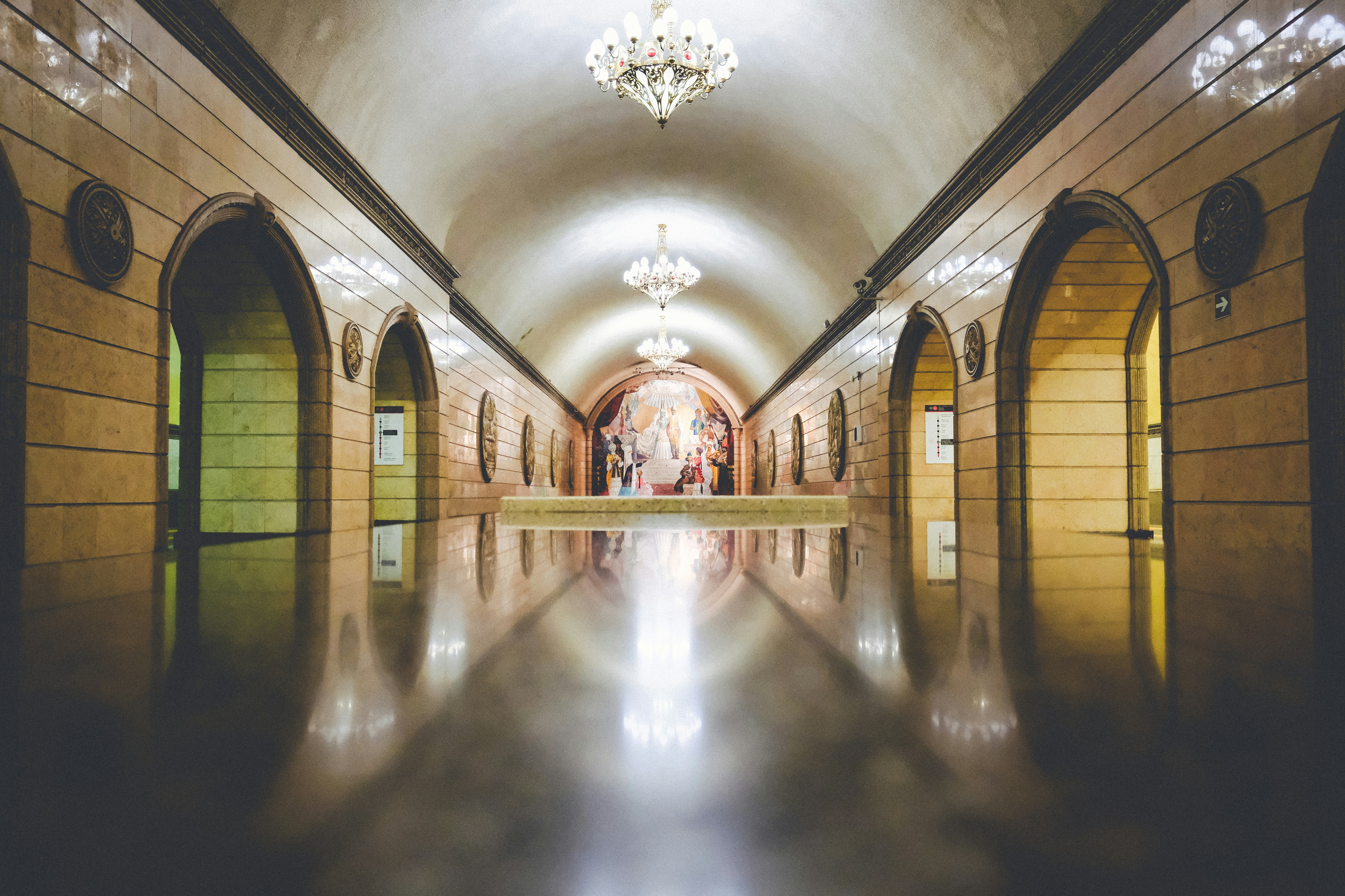 Elegant arched corridor with ornate chandeliers reflecting on a polished floor.