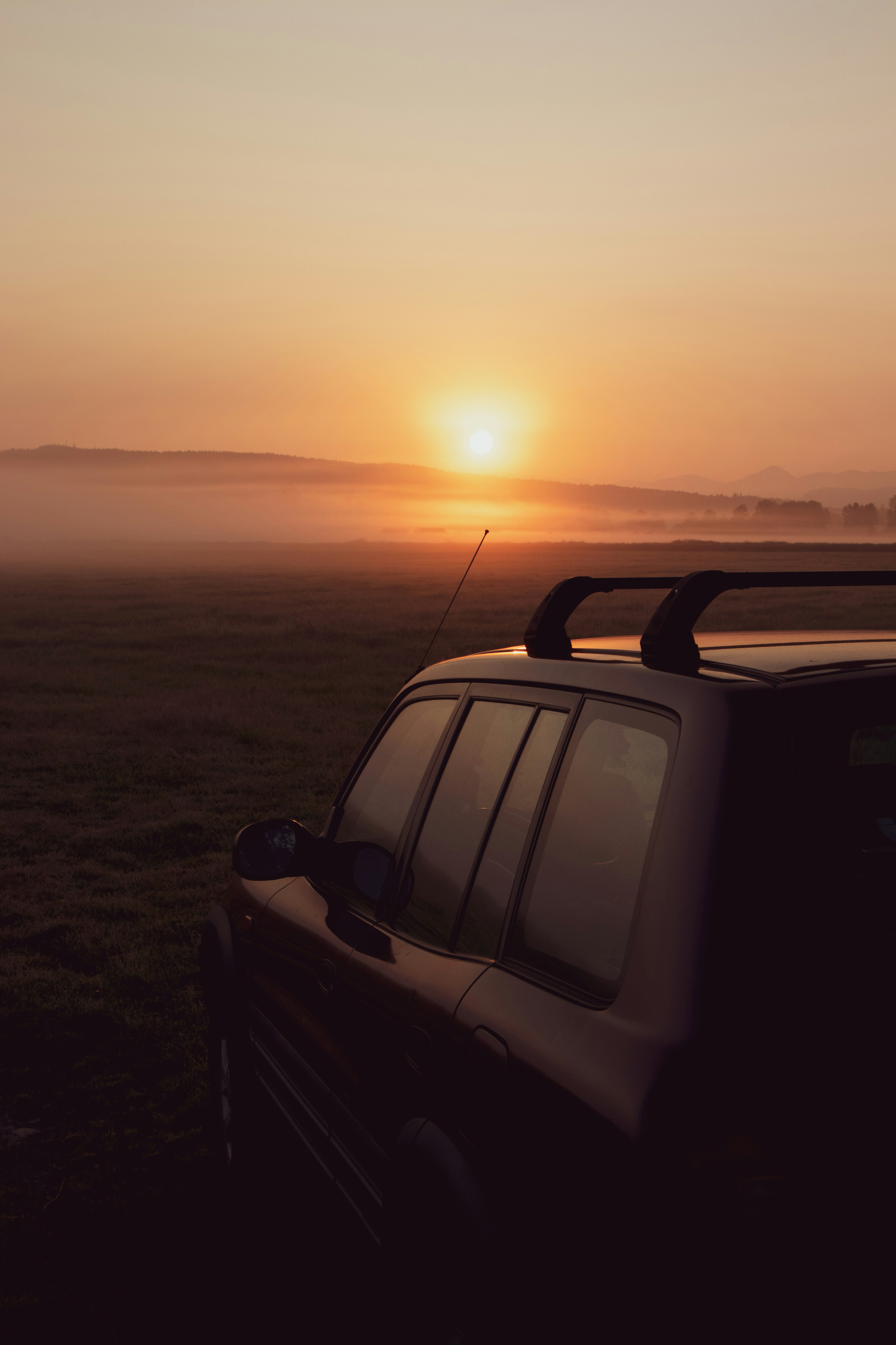 SUV in foreground with rising sun over plain in the distance