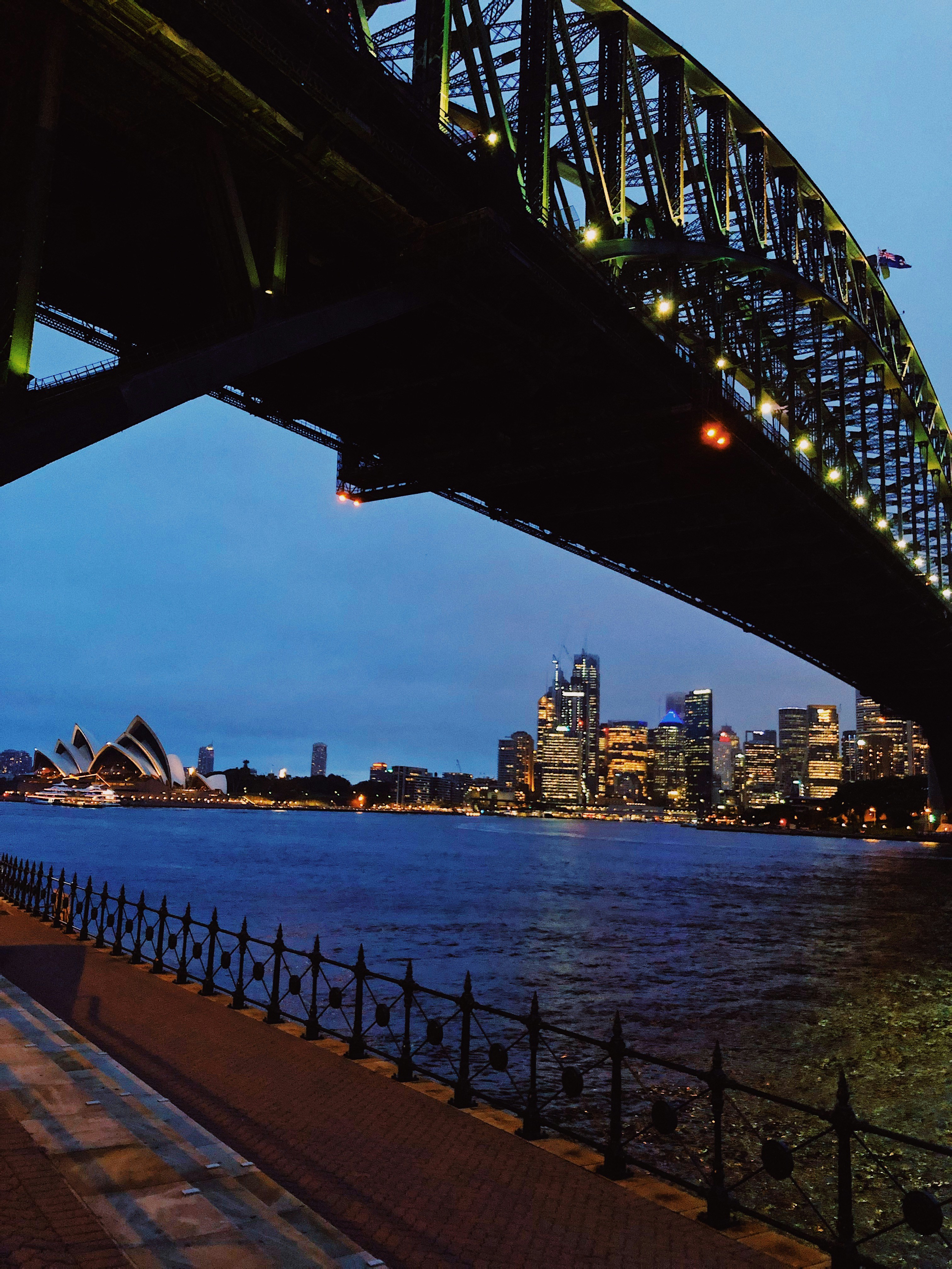 Sydney Harbour Bridge illuminated at dusk, casting shadows over the water with the city skyline in the background.