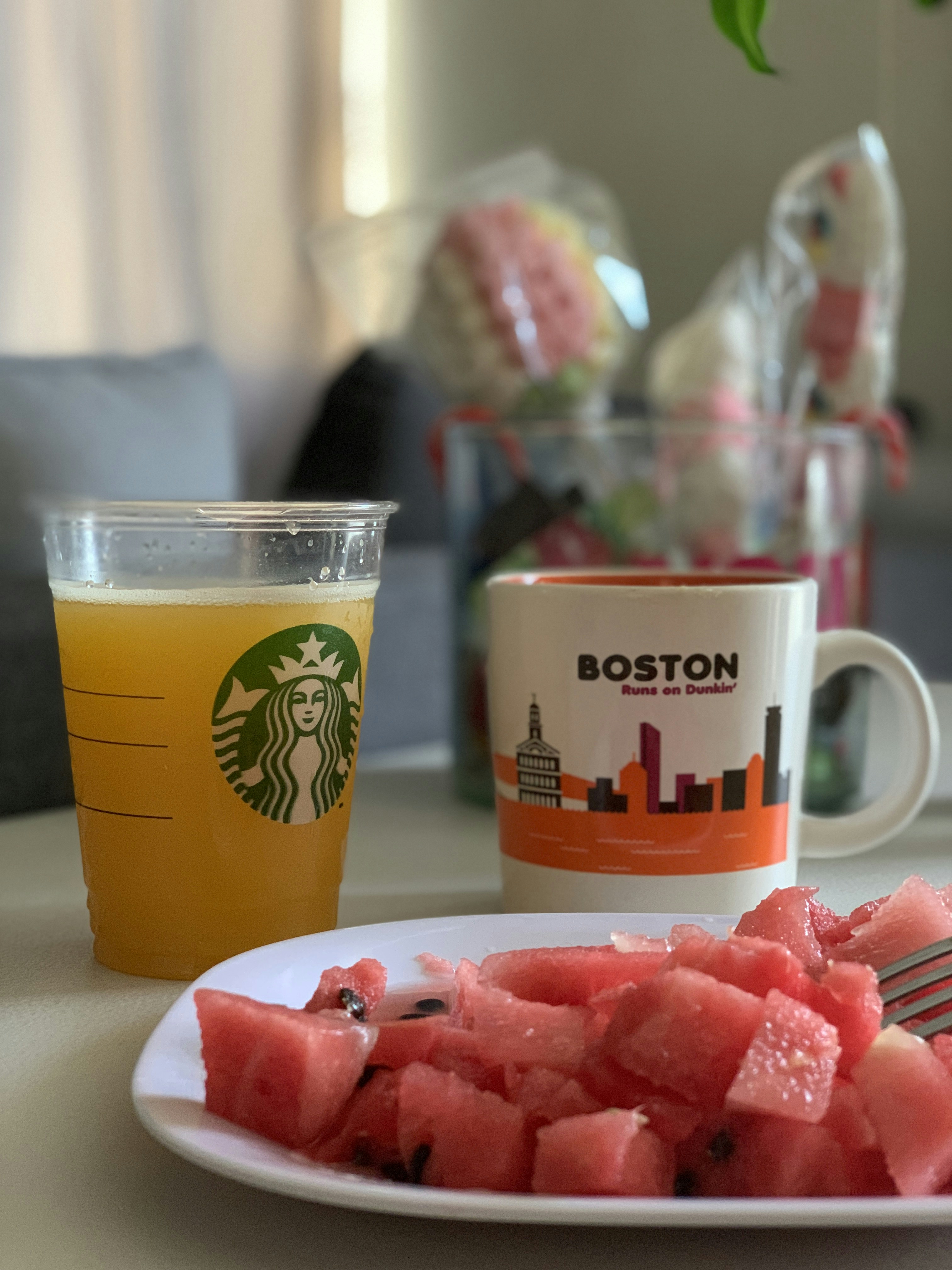 Sliced watermelon on a plate with a Boston-themed mug and orange juice on a table.