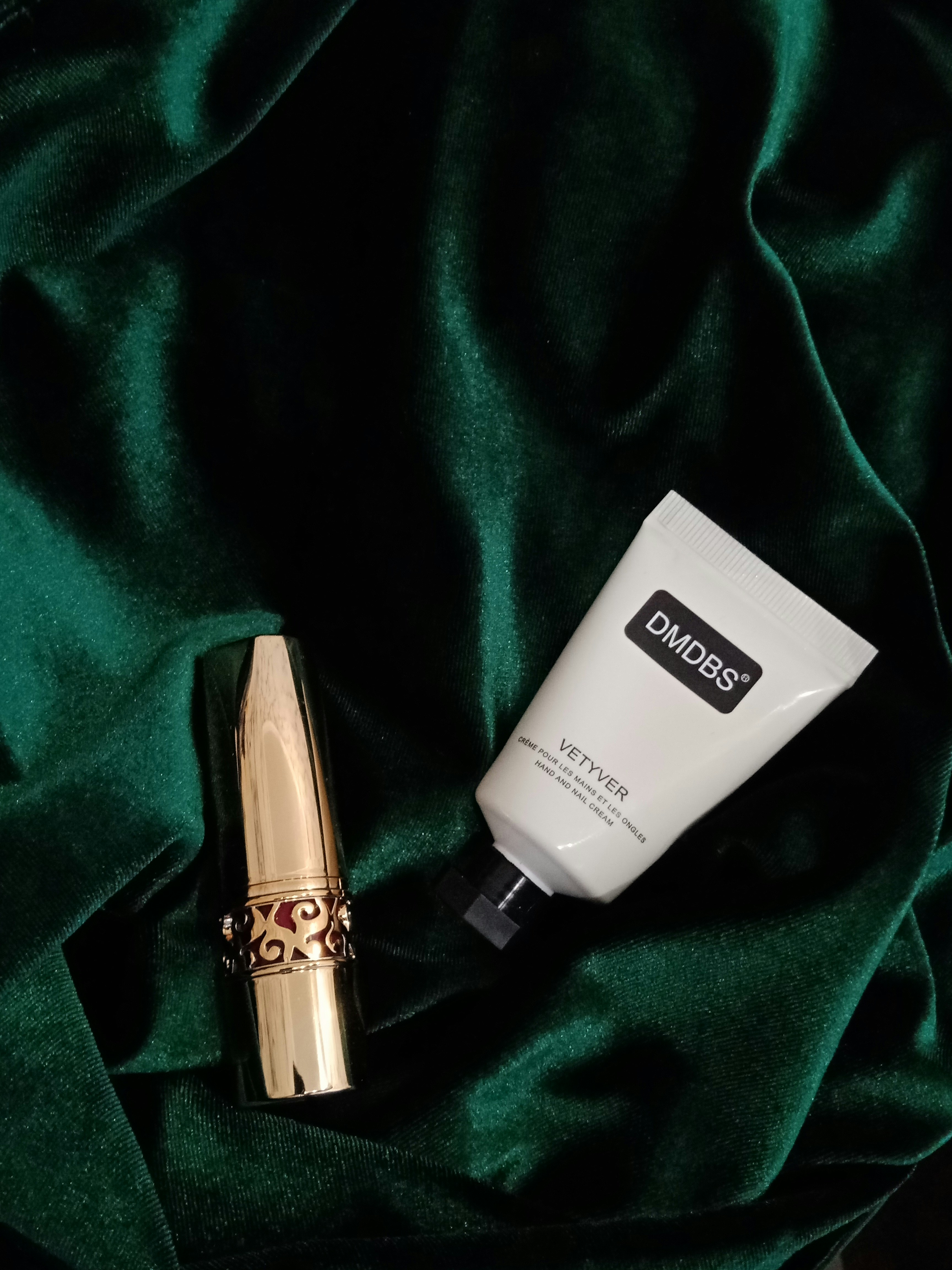 Gold lipstick and a white cream tube arranged on rich green fabric, highlighting luxury and beauty essentials.