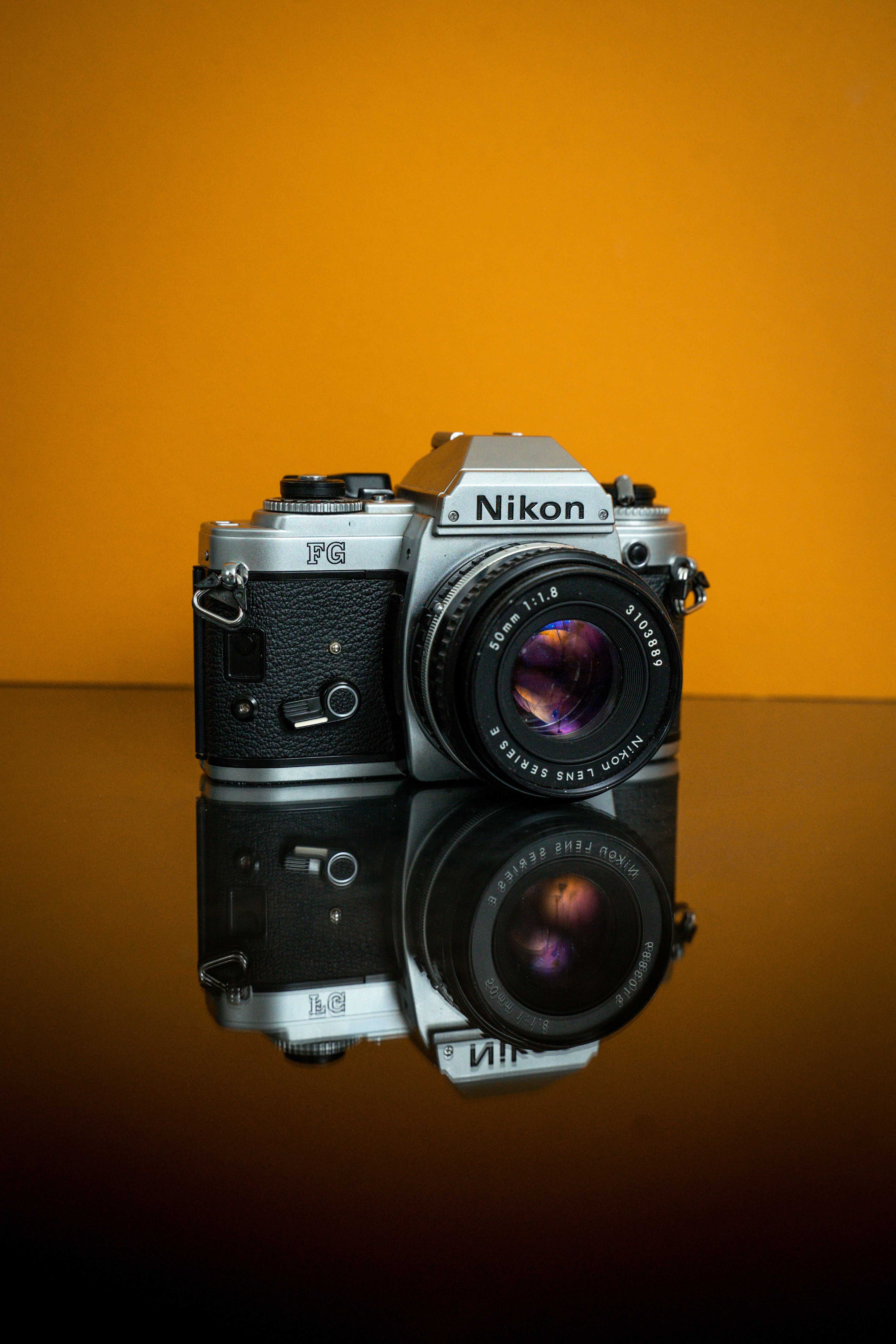 Classic Nikon FG camera with a reflective surface, set against a vibrant orange backdrop.