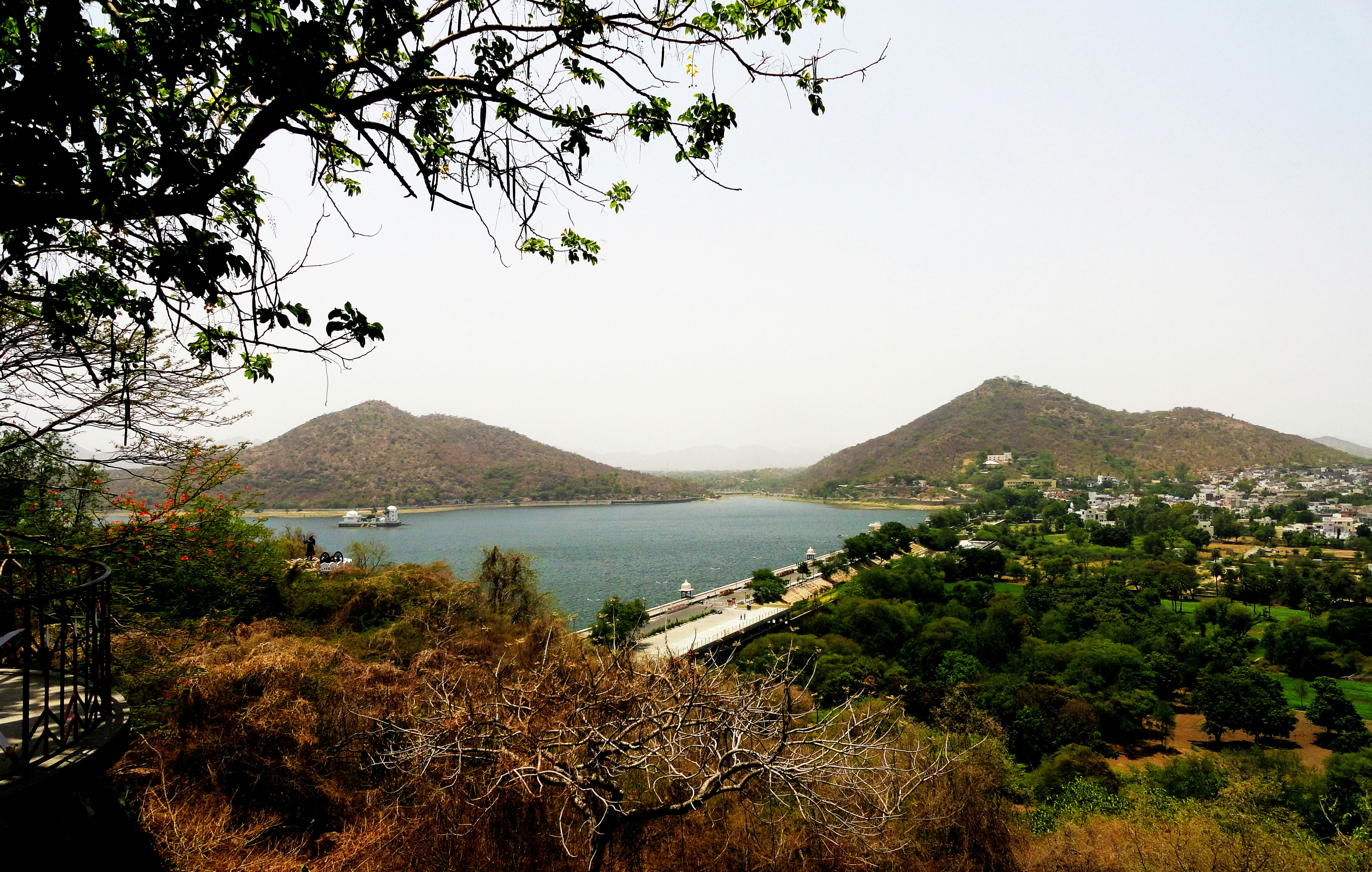 Lake nestled between two hills under a clear sky, surrounded by lush greenery and scattered buildings.