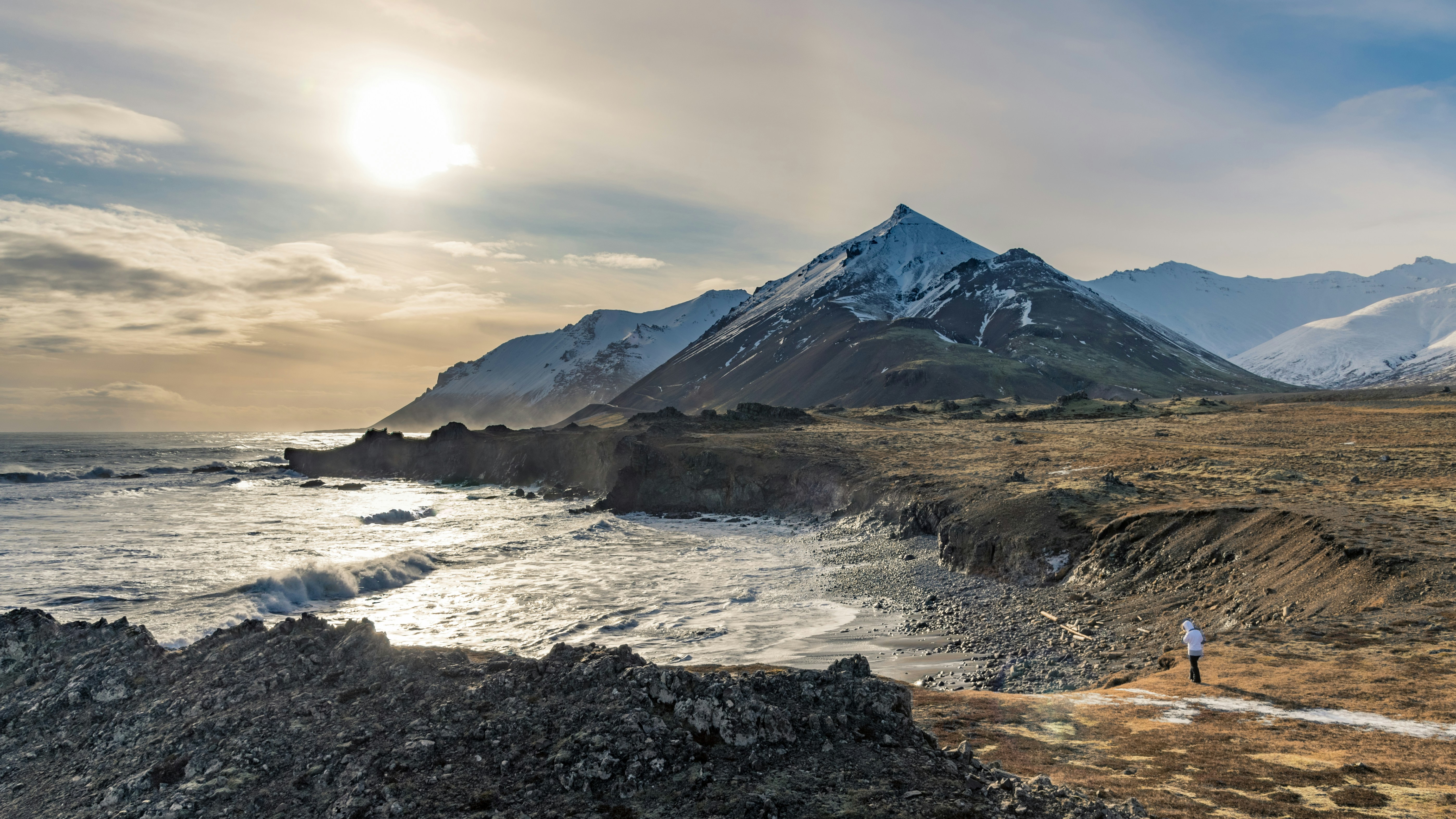 Sunlit Ridge: Coastline, Snow-dusted Peaks, and a Lone Walker