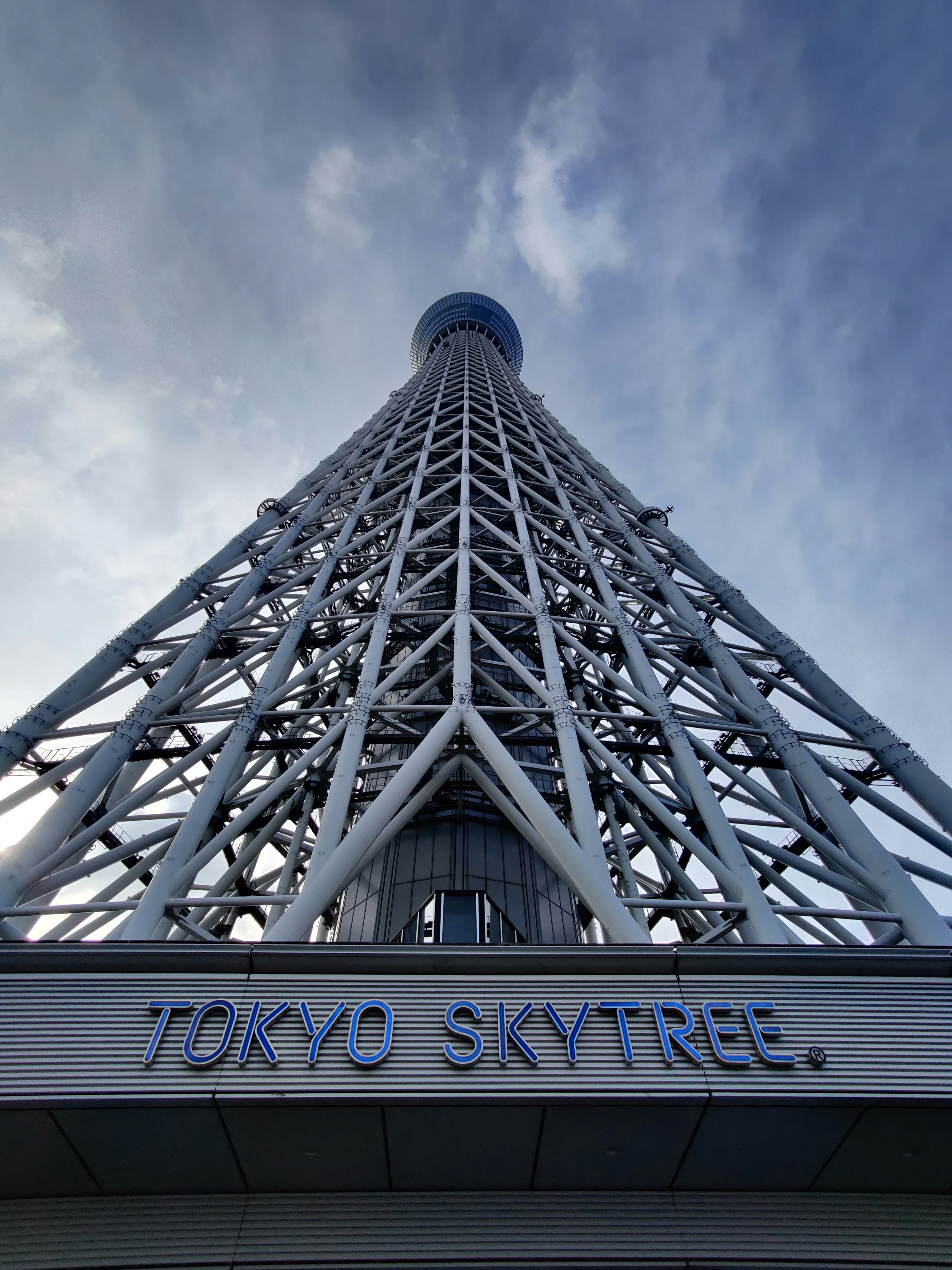 View of Tokyo Skytree from ground level, showcasing its intricate lattice structure against a cloudy sky.