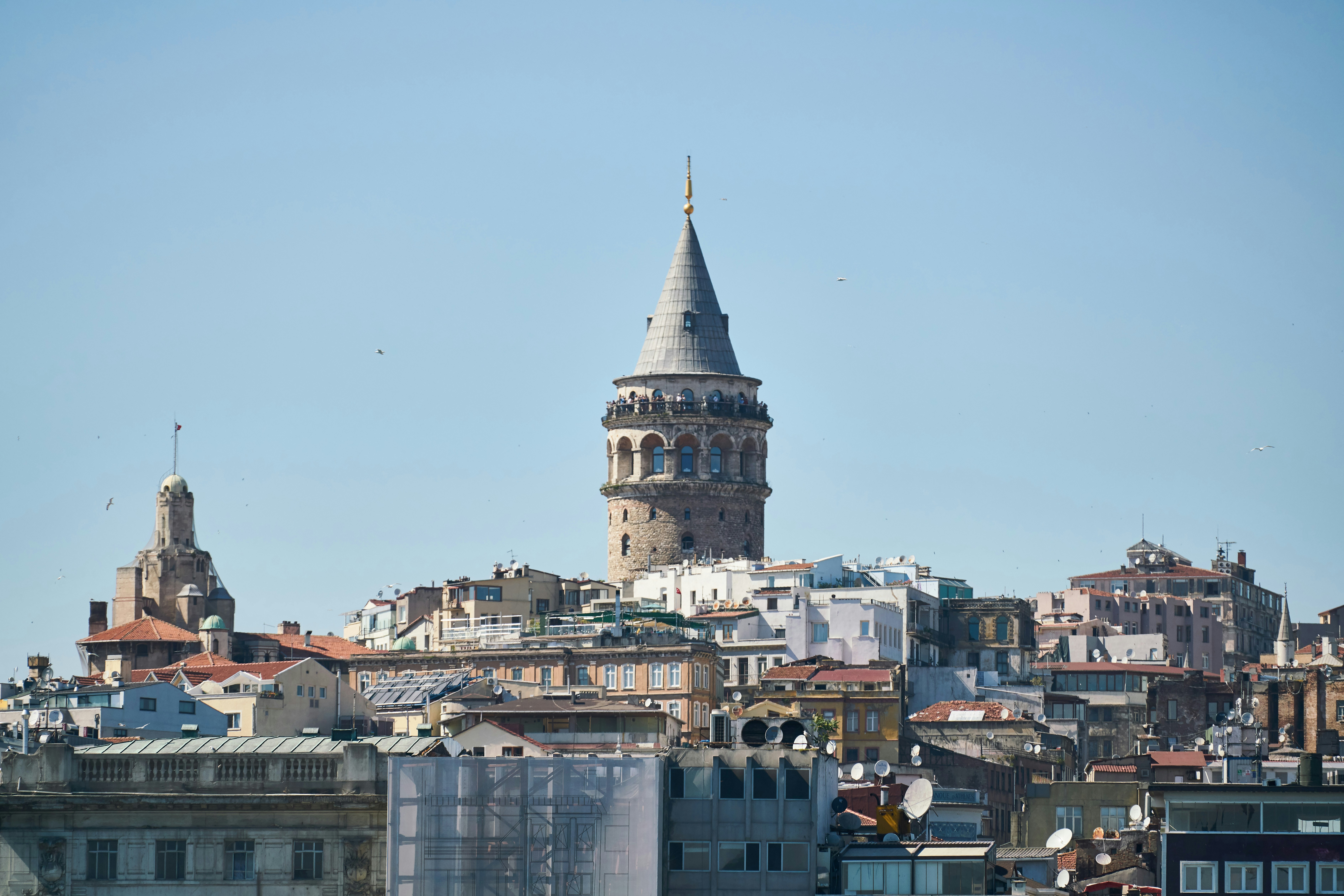 Galata Tower rises prominently above the rooftops of Istanbul, surrounded by a blend of historical and modern architecture.