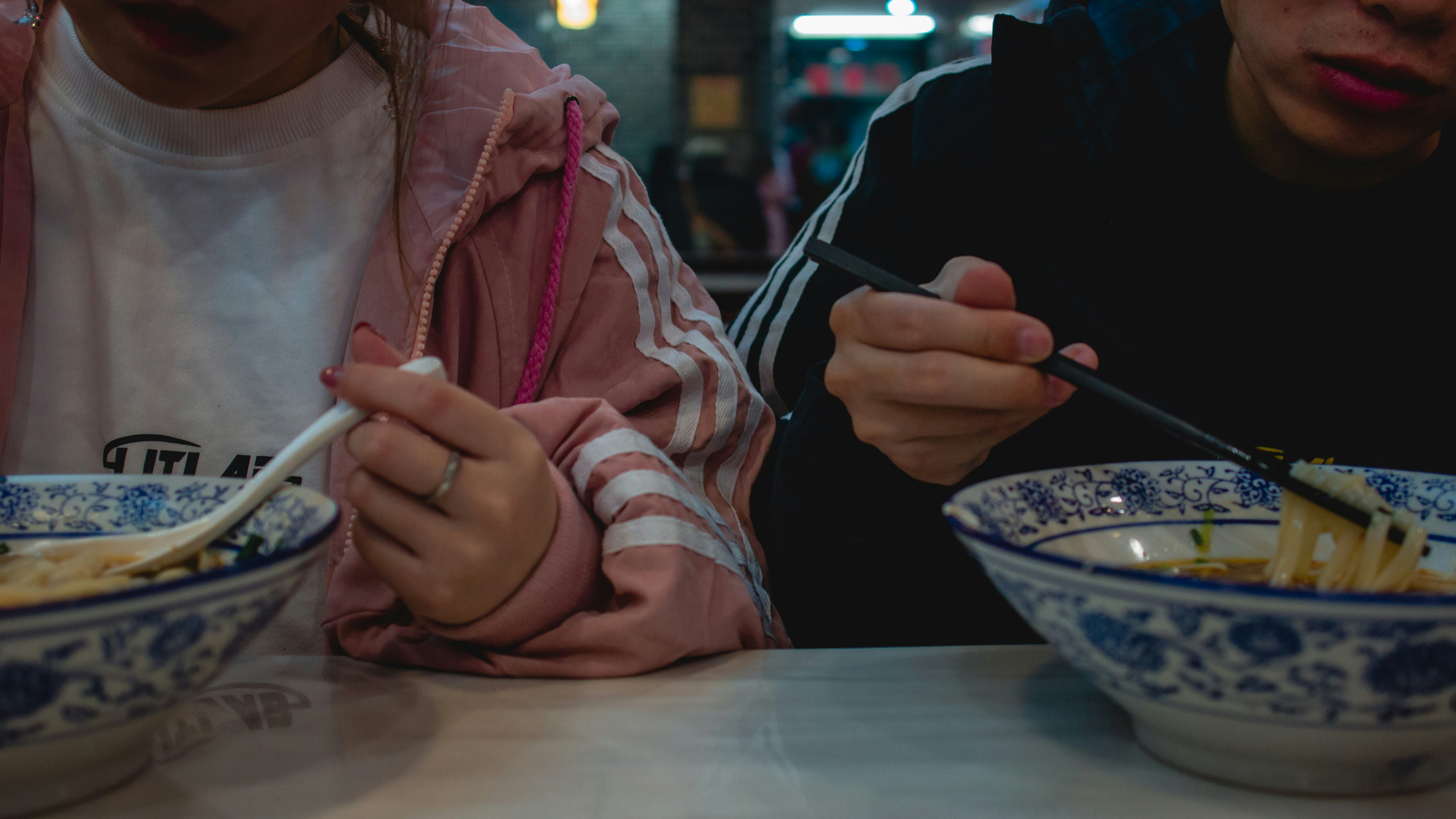 Neon Night Noodles: Hands Hover over Blue-Rimmed Bowls