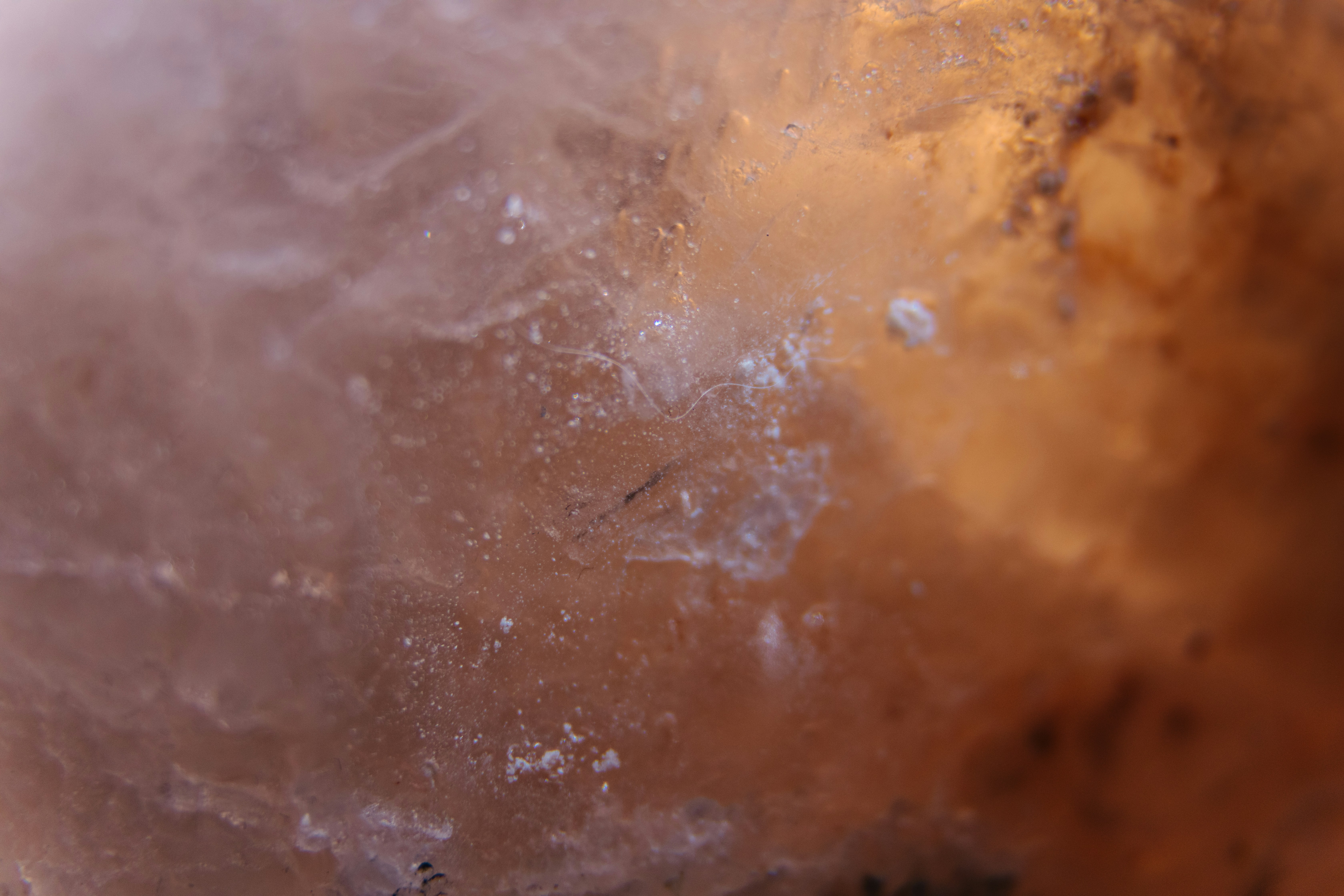 Close-up of a translucent amber stone showcasing intricate textures and natural imperfections. The warm hues and organic patterns highlight its geological beauty.