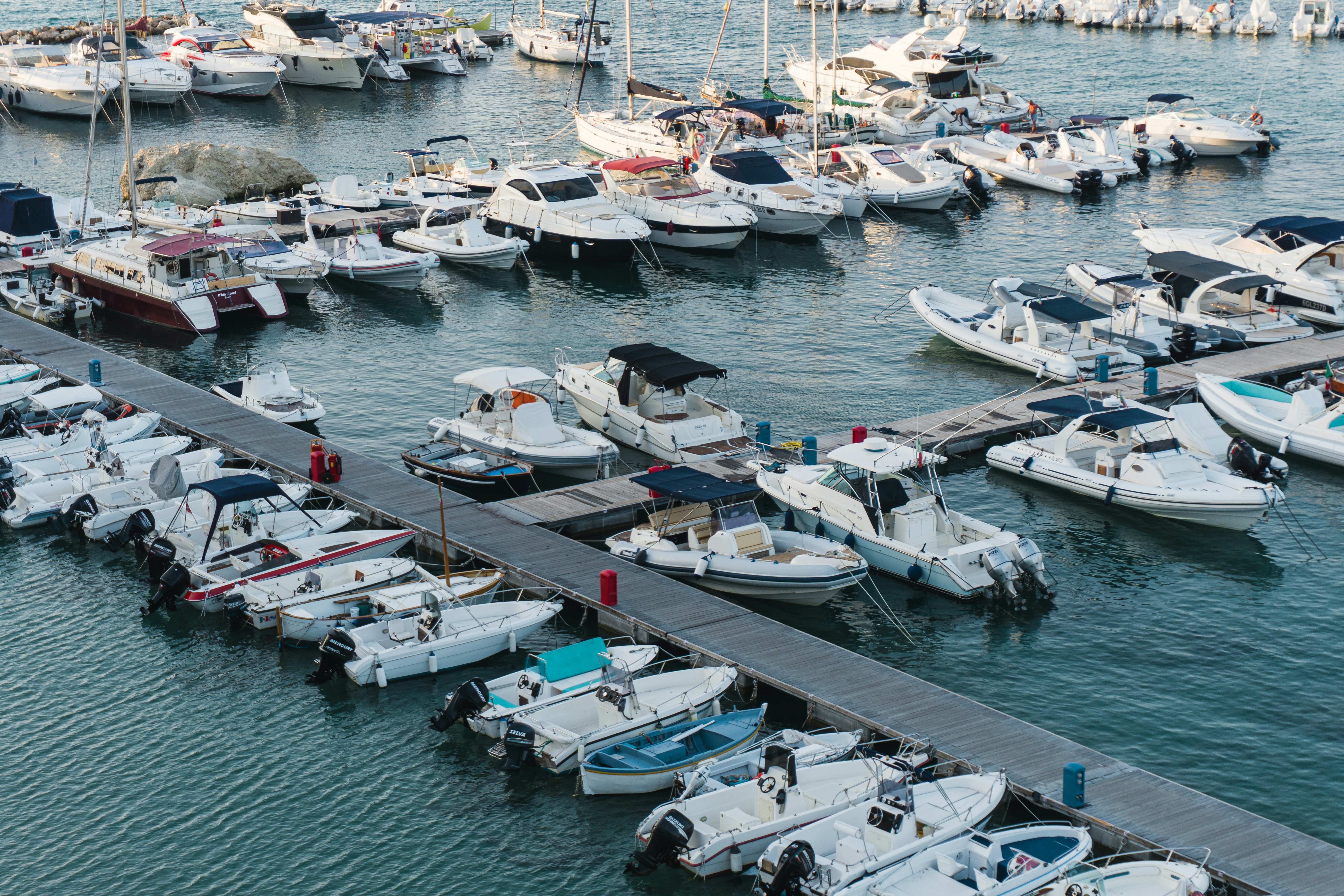 Docked boats lined up in a marina with calm water and a mix of yachts and smaller vessels.