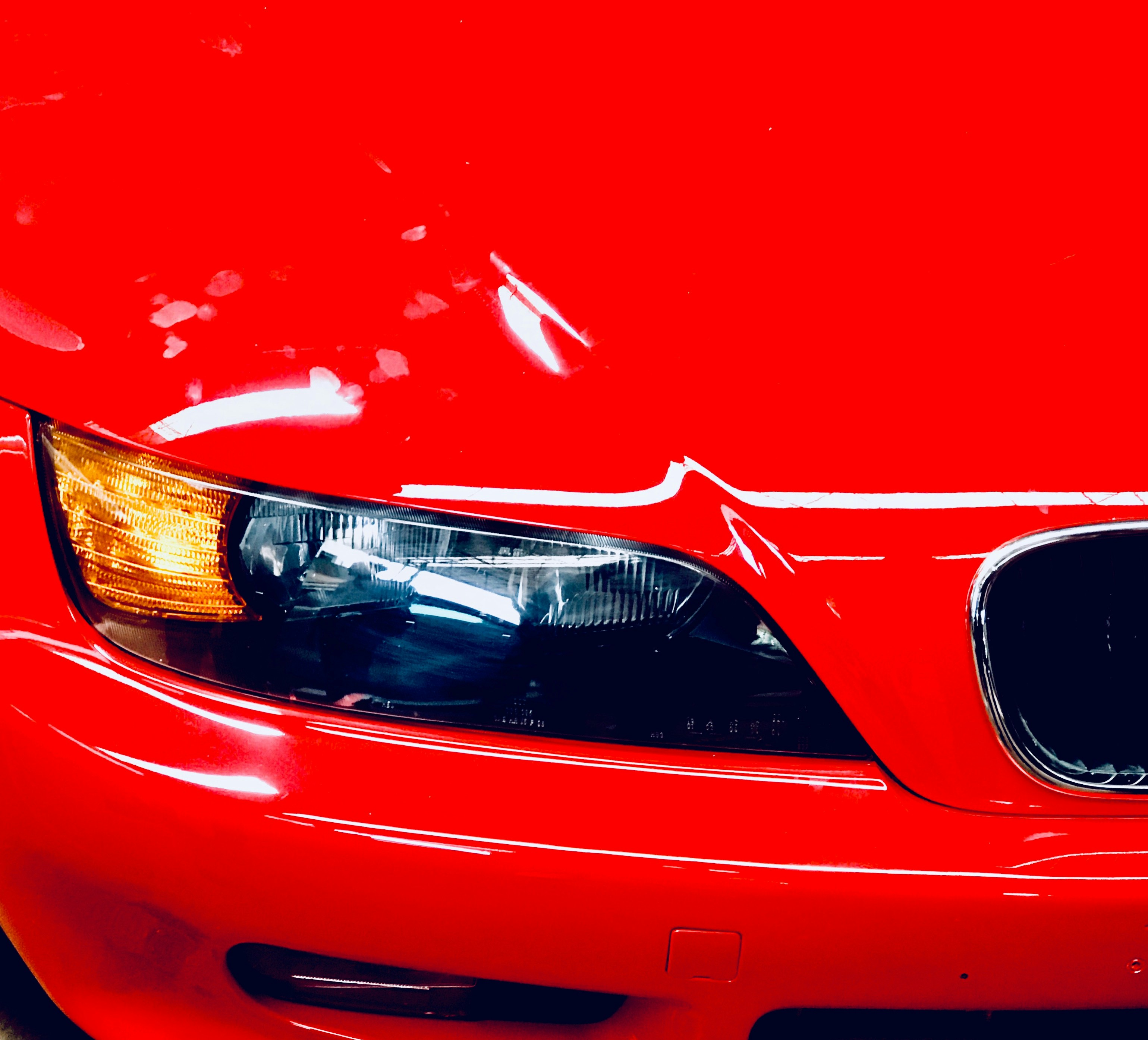 Close-up view of a red car's front, highlighting the sleek headlights and glossy finish. The vibrant color emphasizes the vehicle's design details.