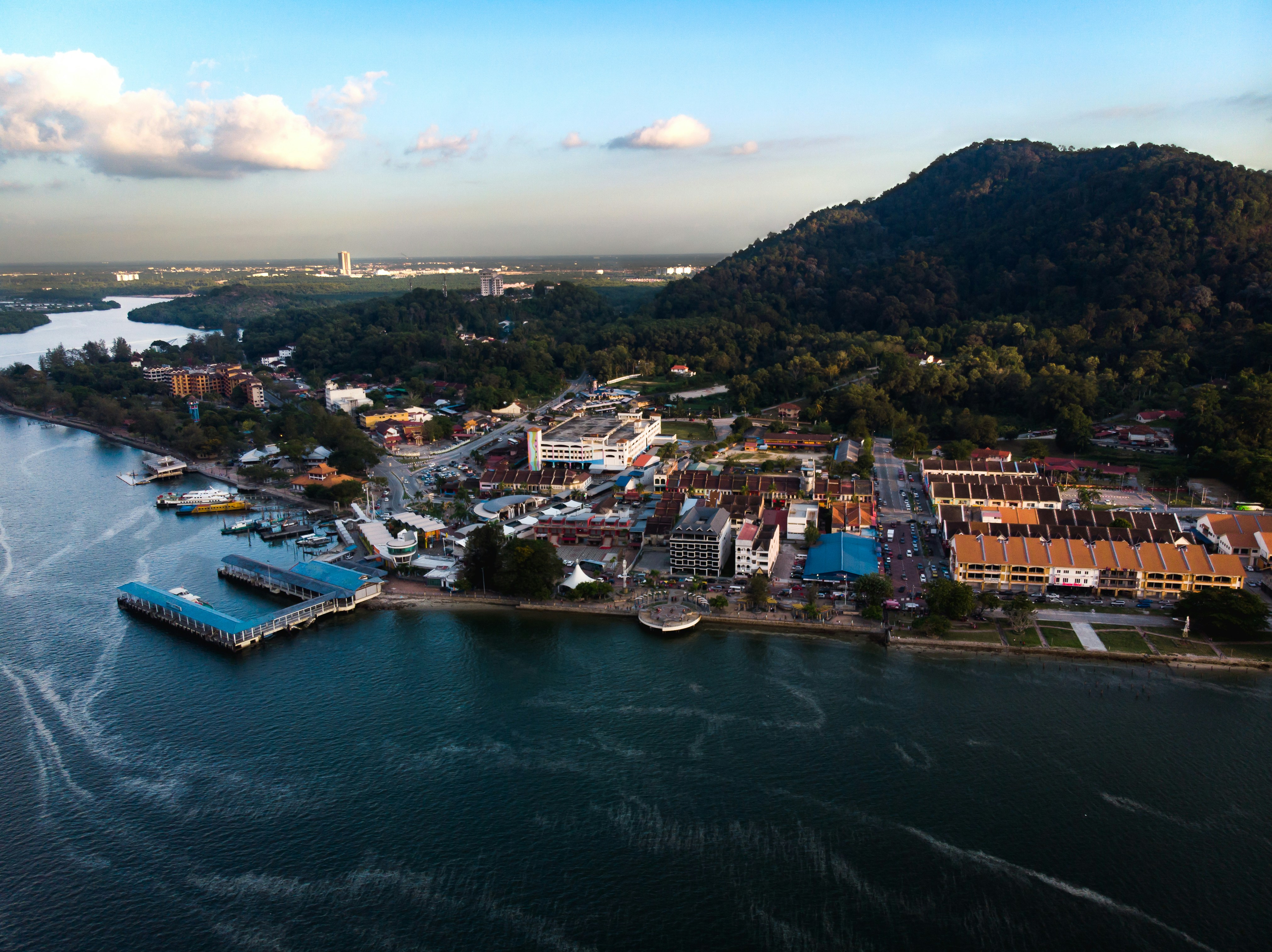 Aerial view of a riverside town with a mountain backdrop and winding river under a clear blue sky.
