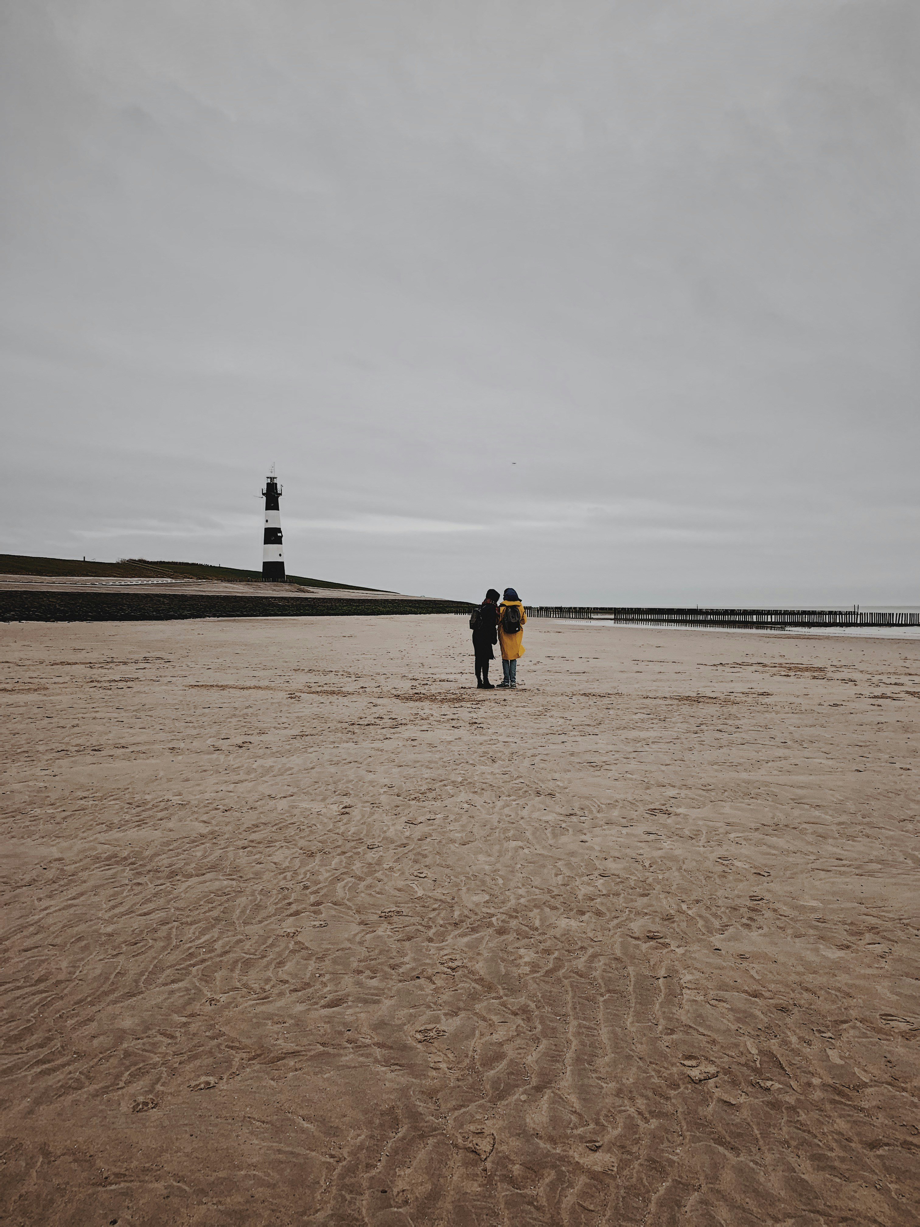man in black jacket standing on brown sand near body of water during daytime