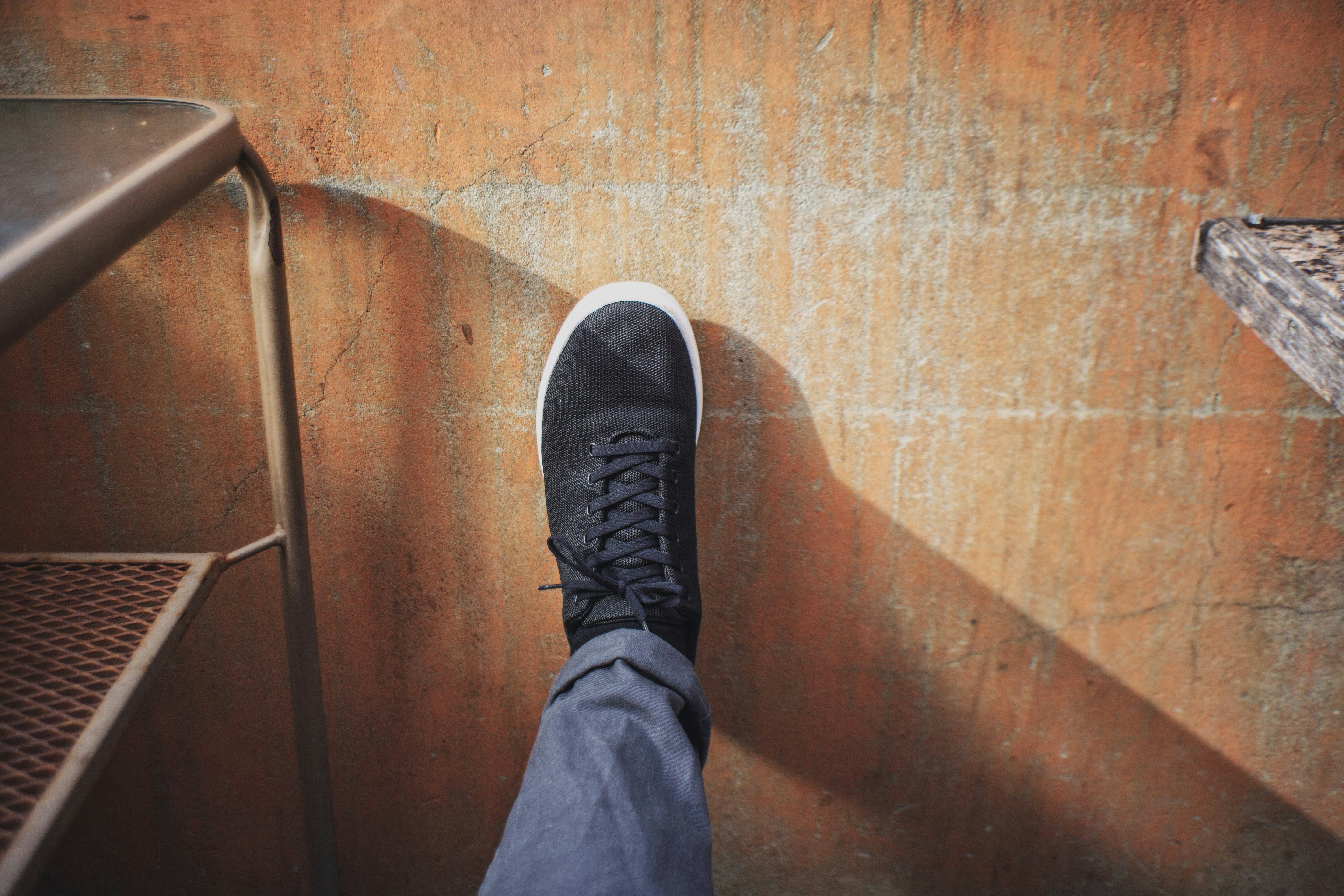 A black sneaker resting on a textured wall, capturing a moment of urban stillness. The interplay of light and shadow adds depth to the scene.