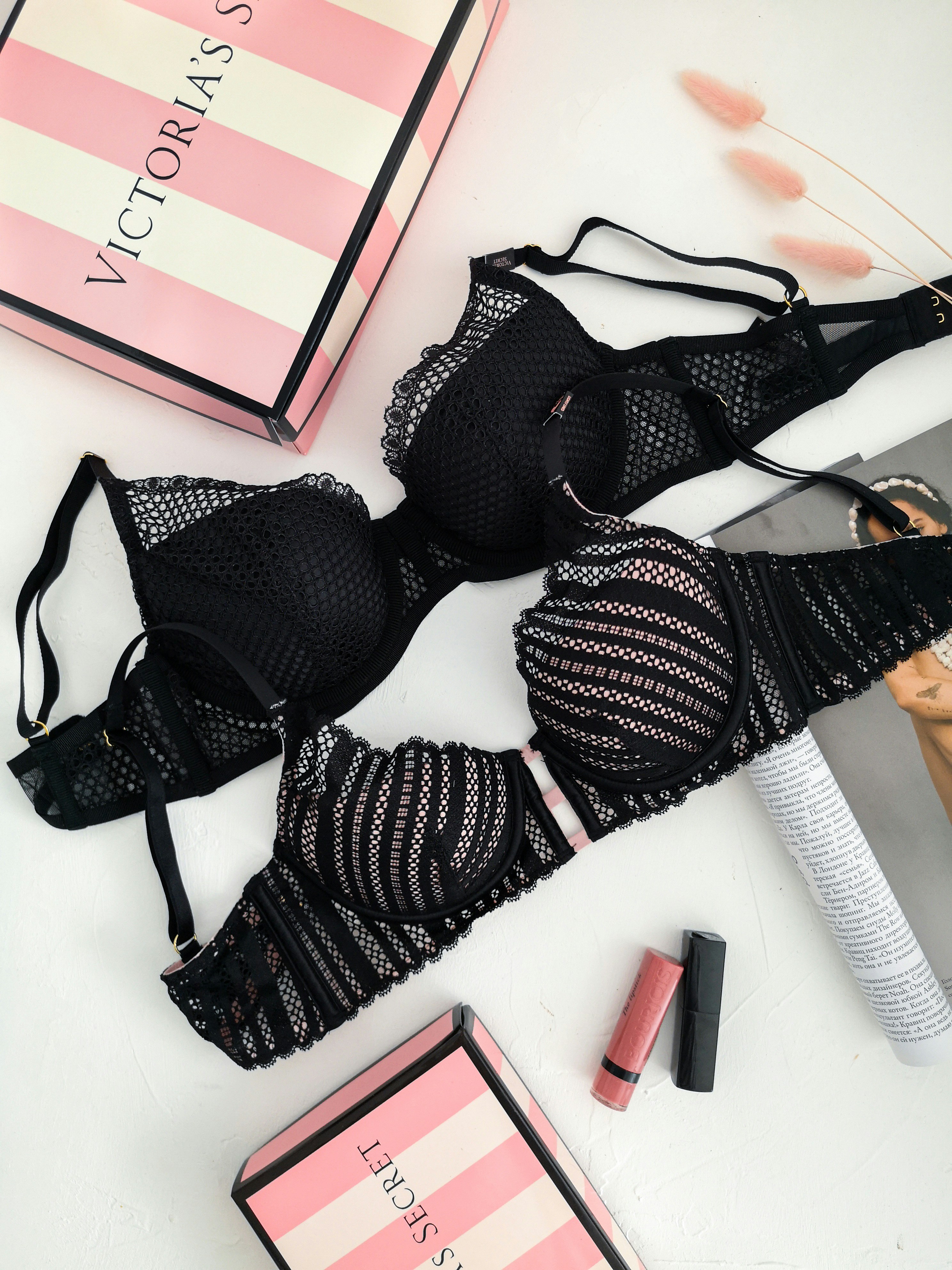 Two intricately designed black bras displayed alongside a Victoria's Secret box and cosmetics, showcasing a blend of fashion and beauty.