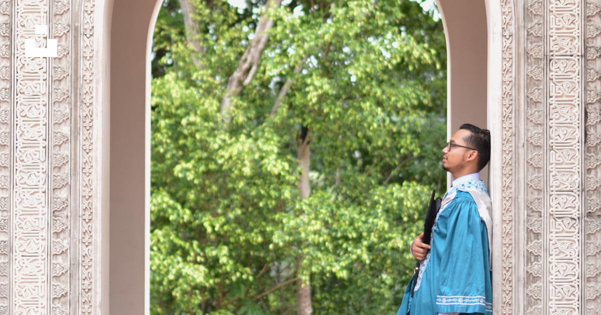 Man In Blue Jacket Standing Near White And Brown Concrete Building During Daytime Photo Free