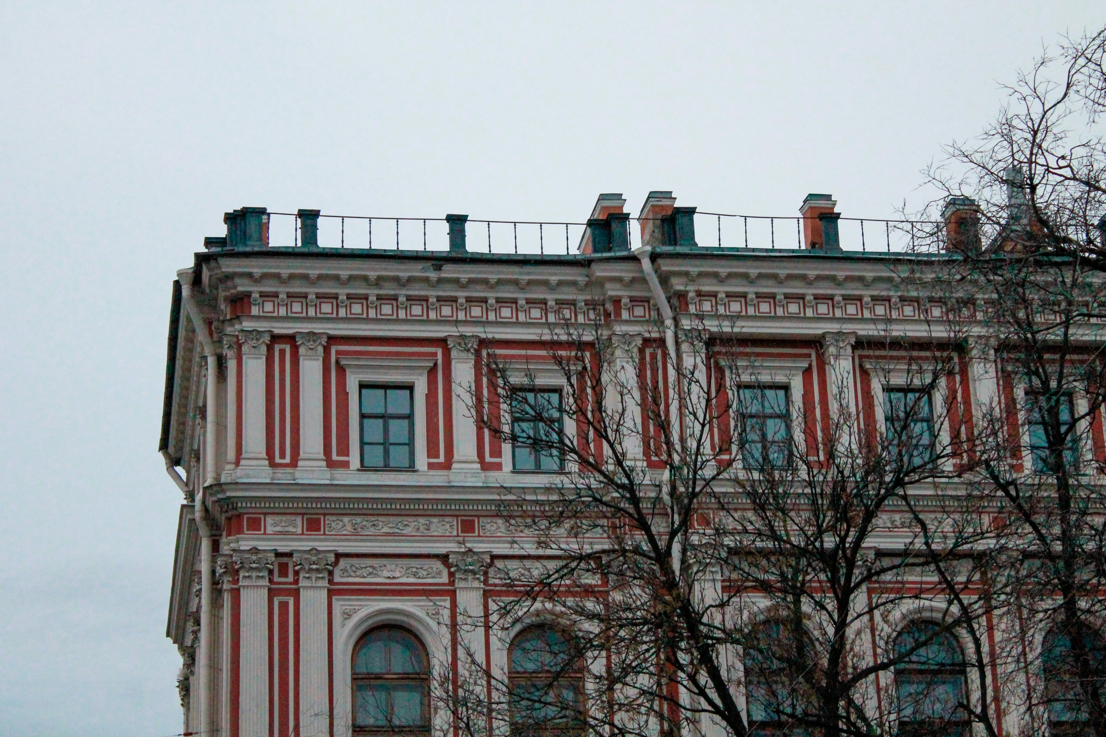 Ornate building facade adorned with intricate red and white patterns, framed by bare tree branches against a gray sky.