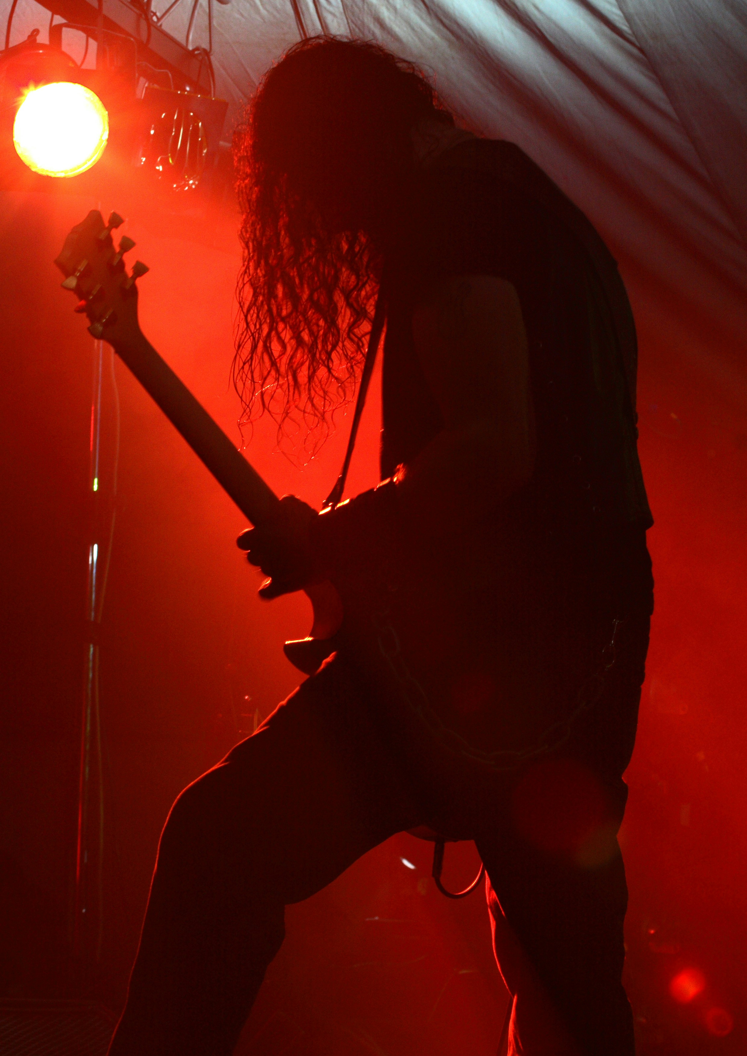 Backlit silhouette of a guitarist with a diagonal guitar neck amid red stage smoke. The scene emphasizes mood and form over detail.