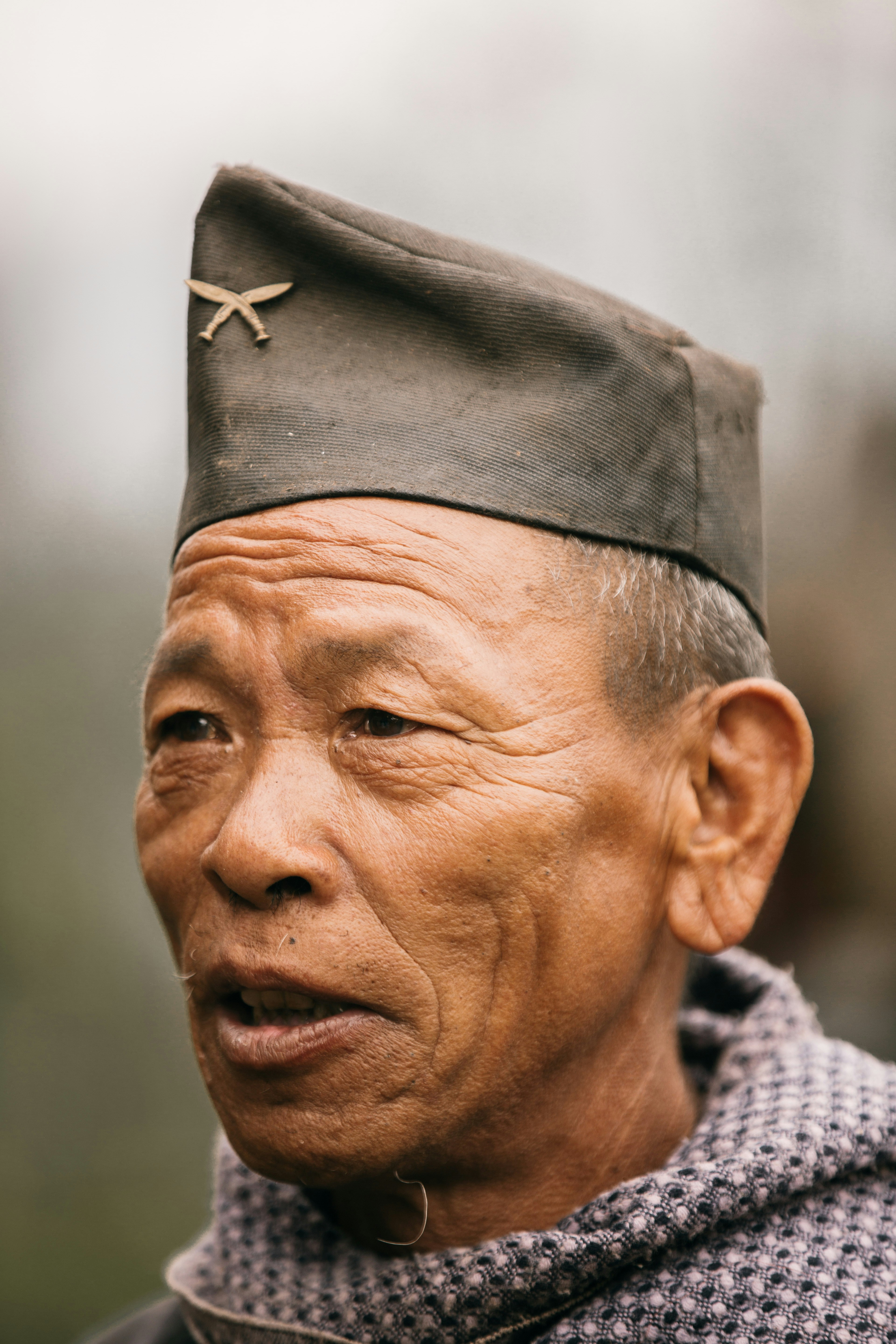 Elderly man with a weathered face and traditional hat, expressing a moment of contemplation. The focus is on his expressive features and the texture of his skin.