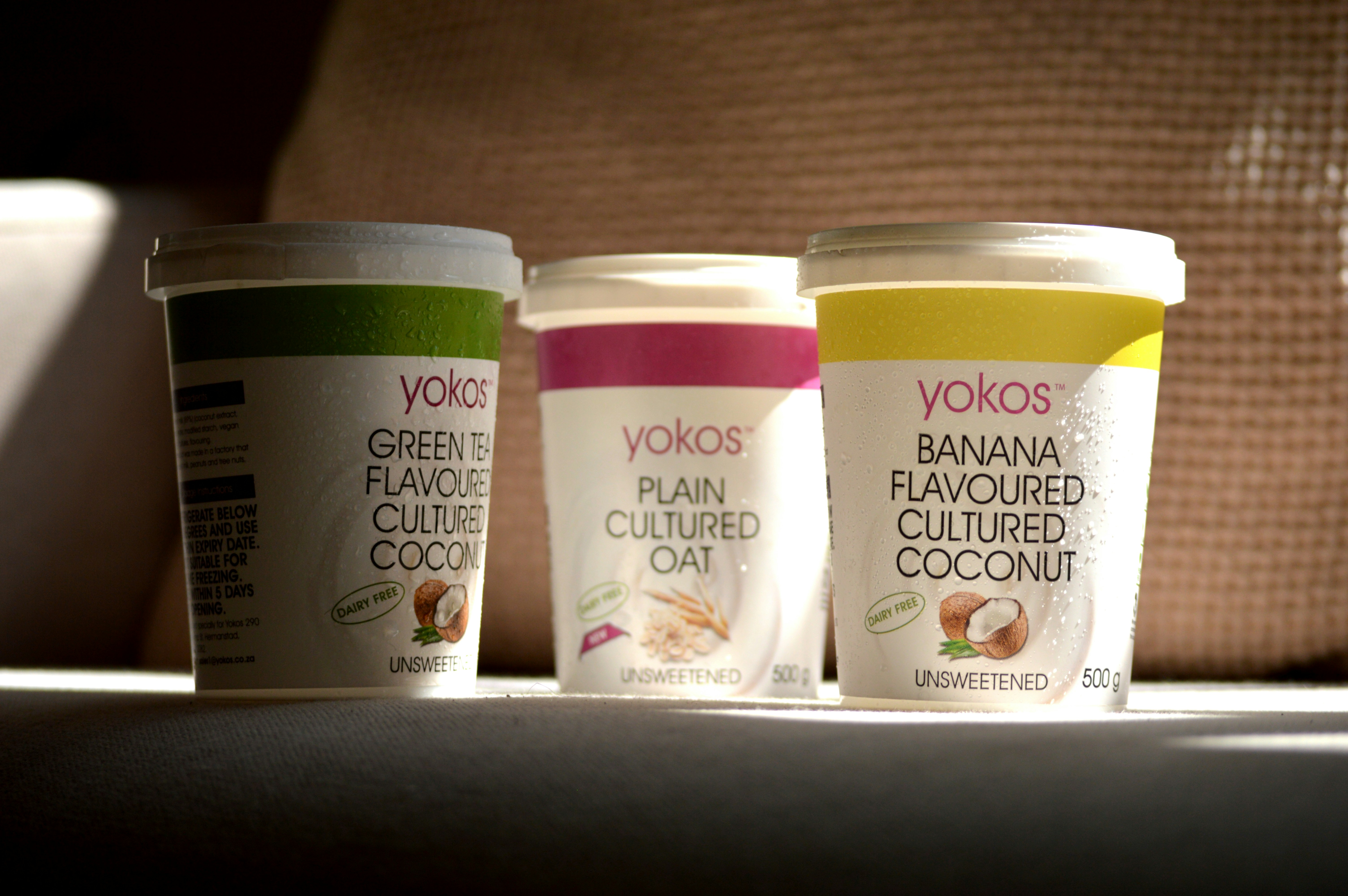 Three containers of Yokos cultured coconut products arranged in natural light, showcasing their unique flavors. Each container features a distinct color and label design.