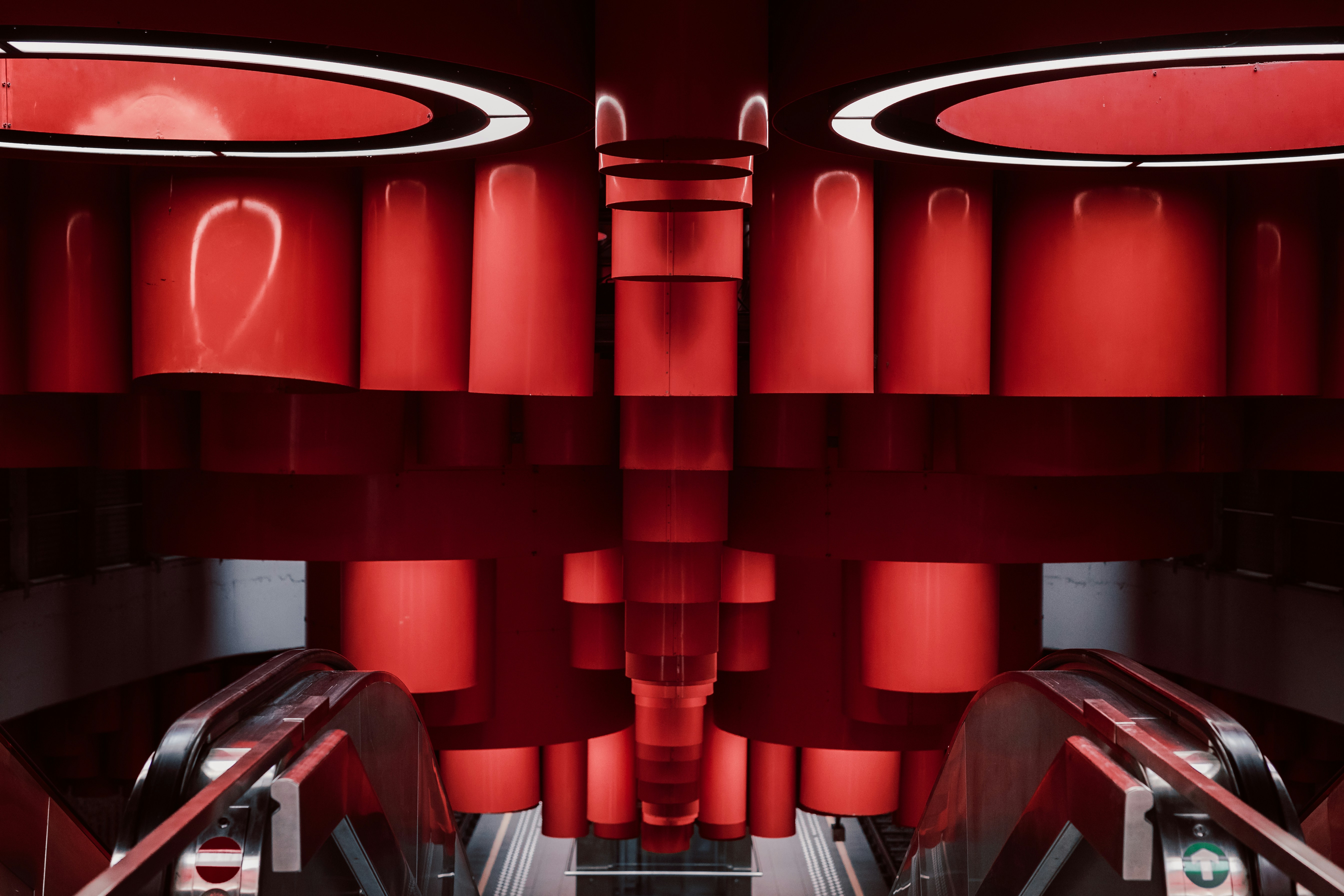Vibrant red cylindrical structures create a dynamic visual experience in a modern architectural space. The interplay of light and shadow enhances the depth and intrigue.