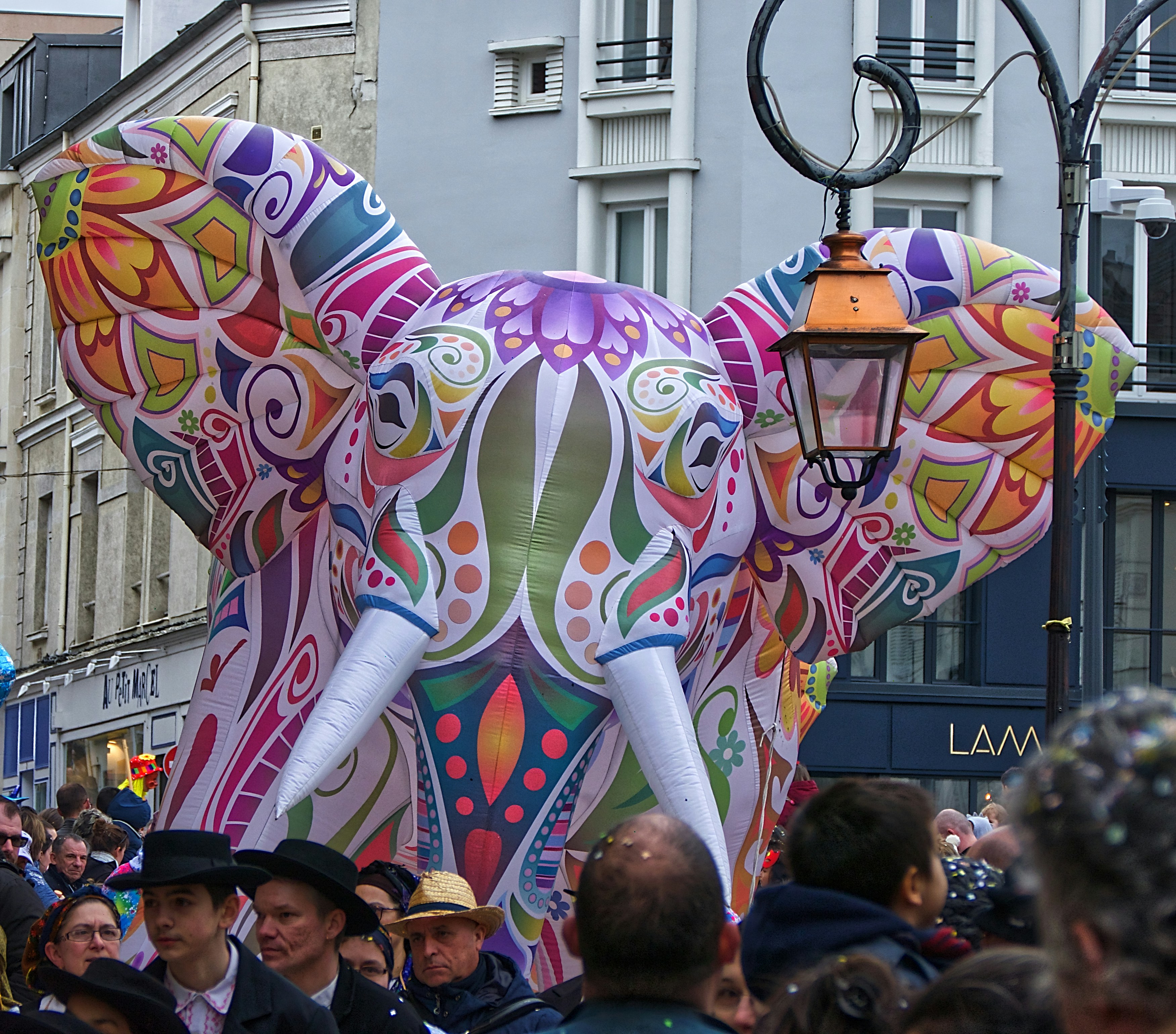 Colorfully decorated elephant sculpture surrounded by a lively crowd during a festive event.
