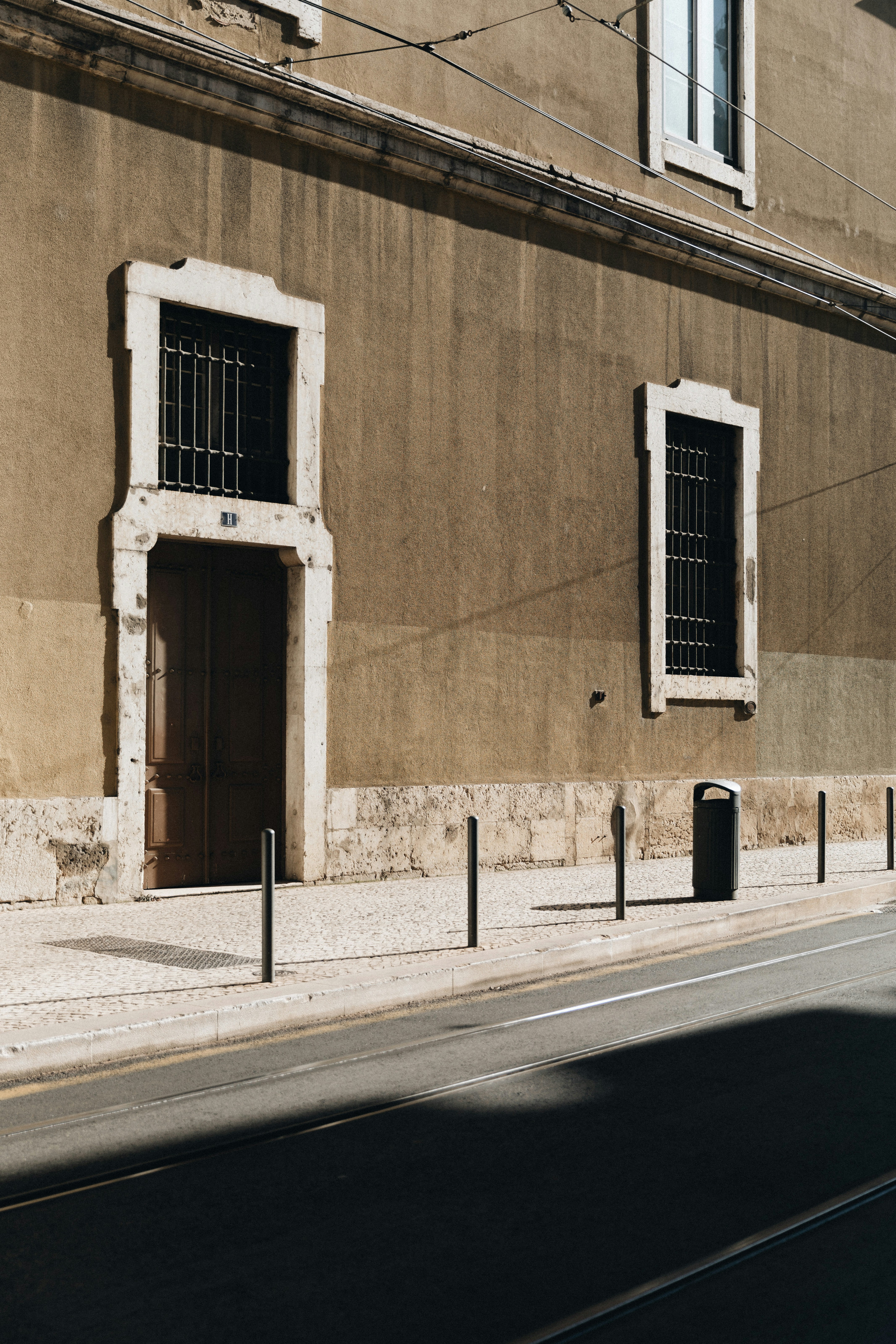 Weathered building wall with a wooden door and barred windows, showcasing architectural details in soft sunlight.