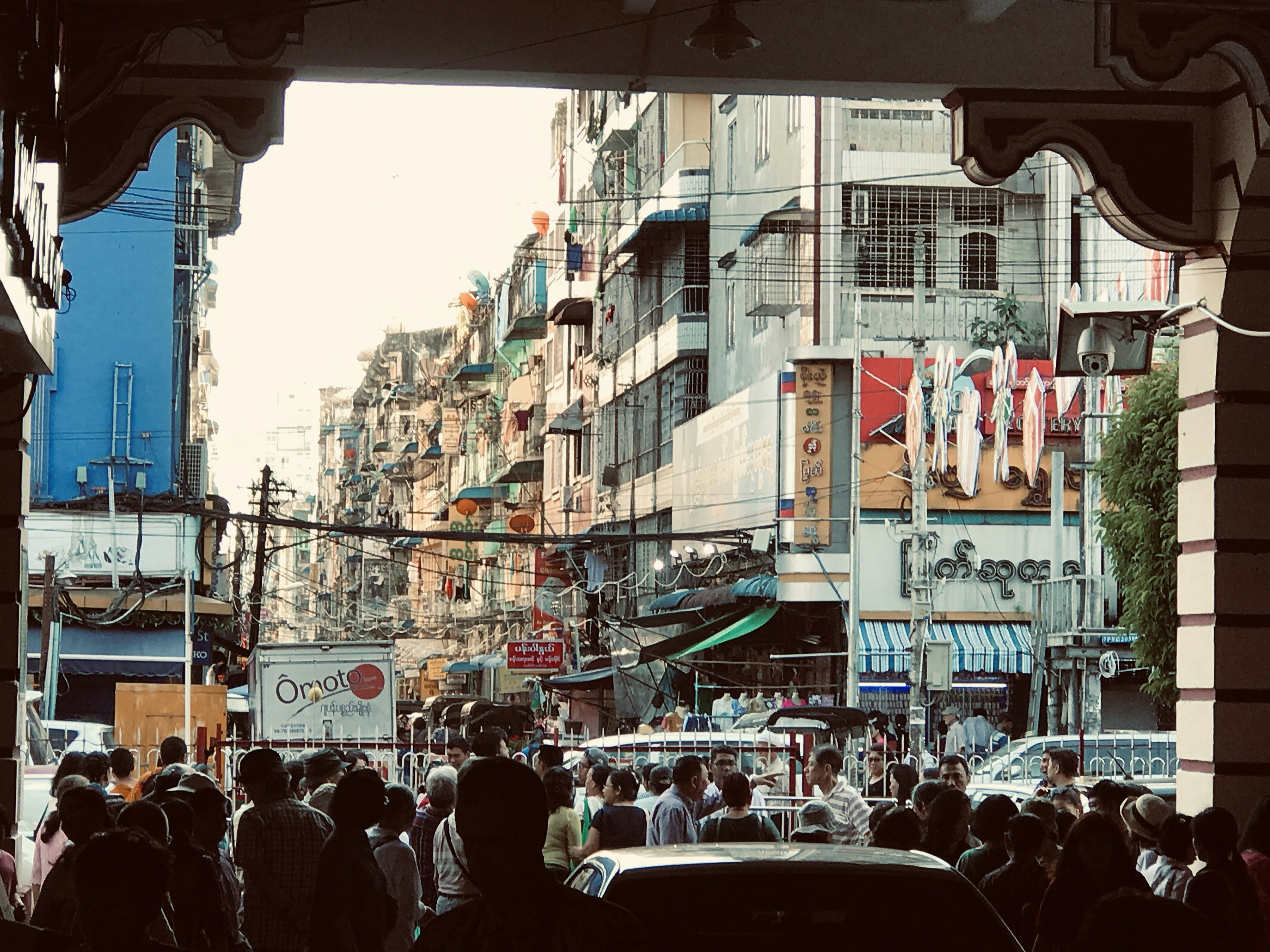 Bustling street scene filled with pedestrians and colorful shopfronts, showcasing the vibrancy of urban life. The view is framed by an architectural archway.