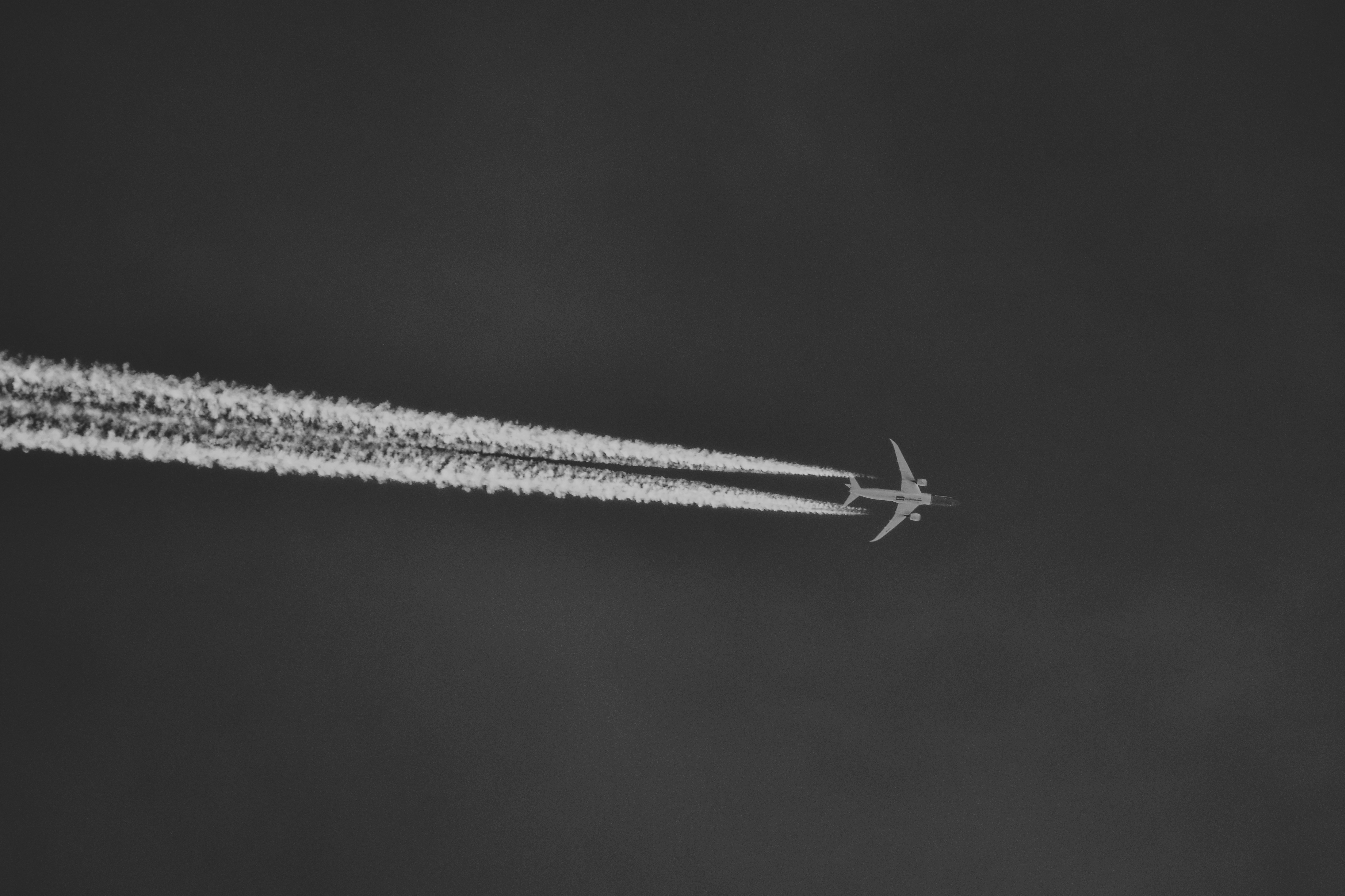 Airplane soaring through a monochrome sky, leaving behind distinct contrails that trace its path.