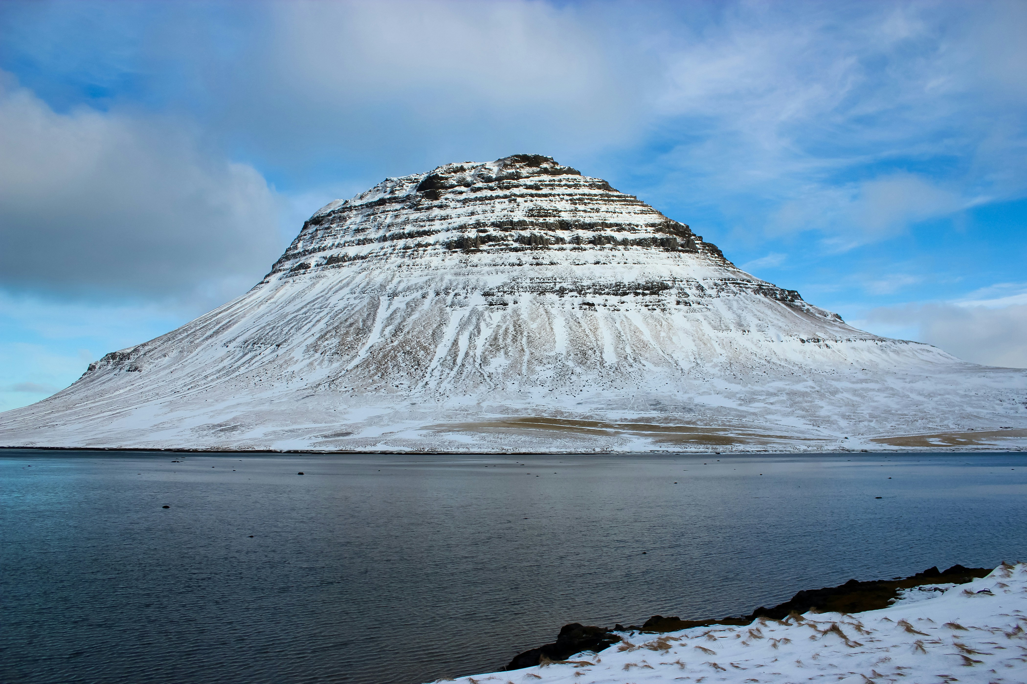 white and brown mountain near body of water under white clouds during daytime