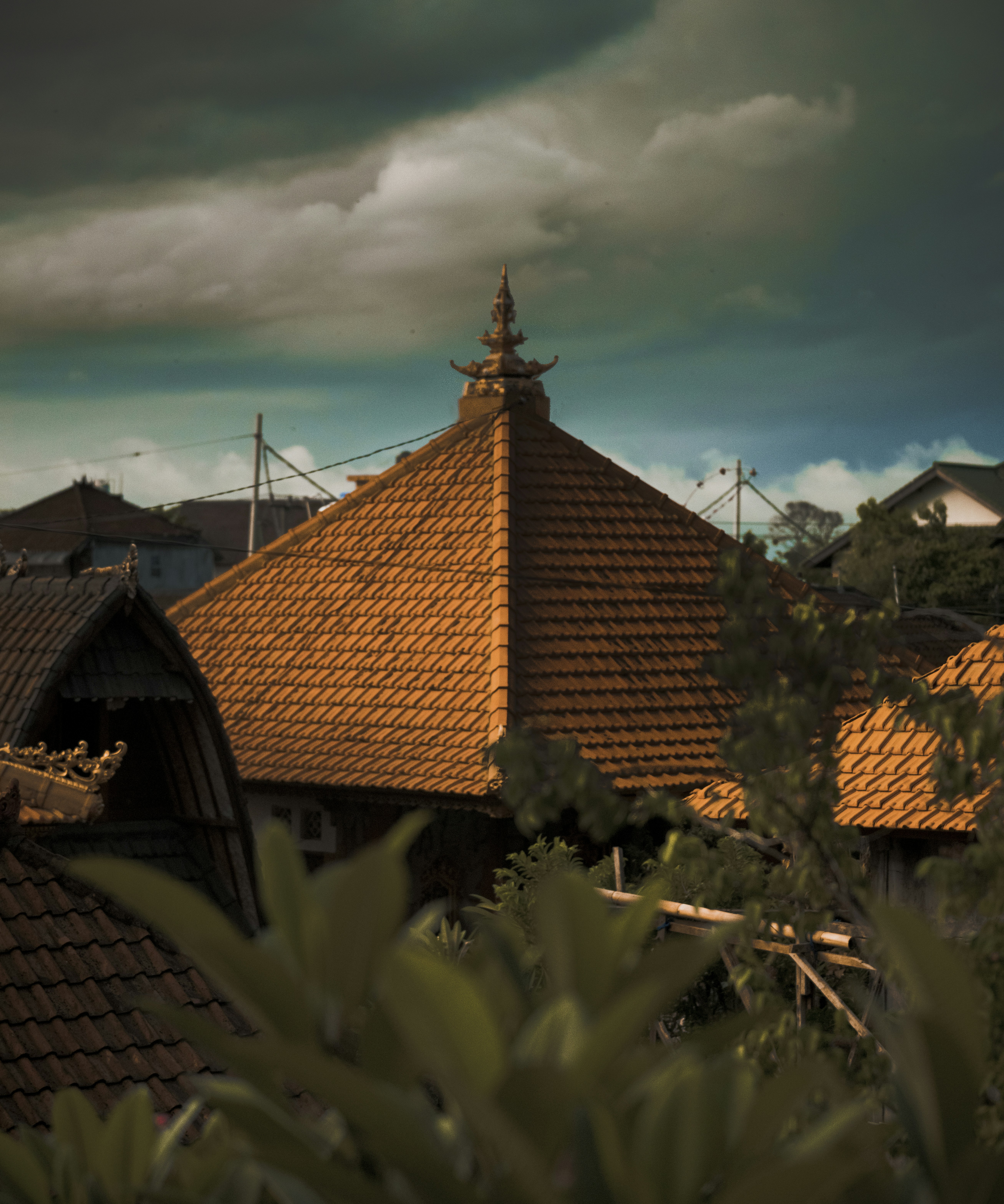 Traditional Balinese rooftops adorned with terracotta tiles, framed by lush greenery under a moody sky.