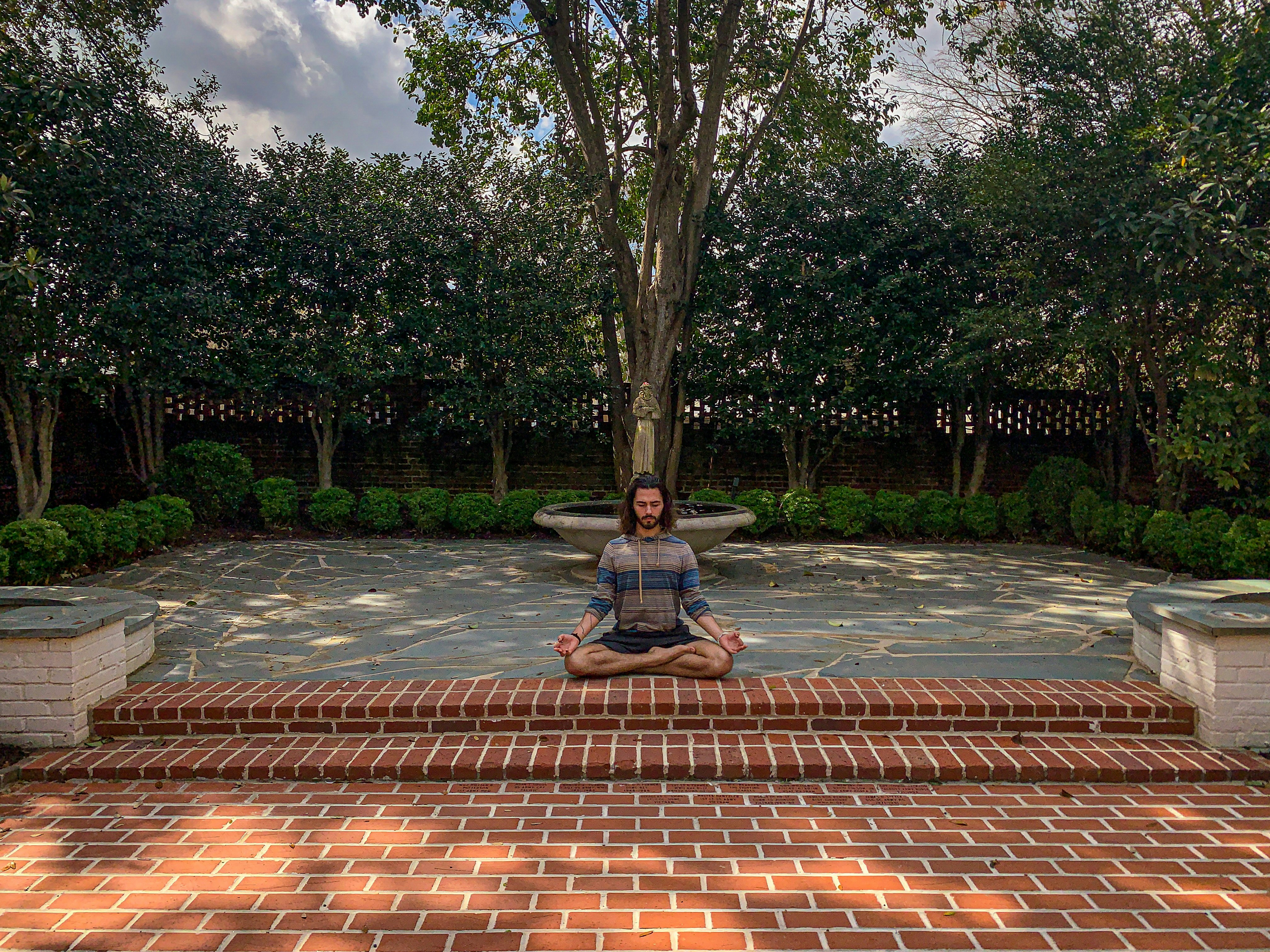 man in blue t-shirt sitting on brown brick floor near green trees during daytime