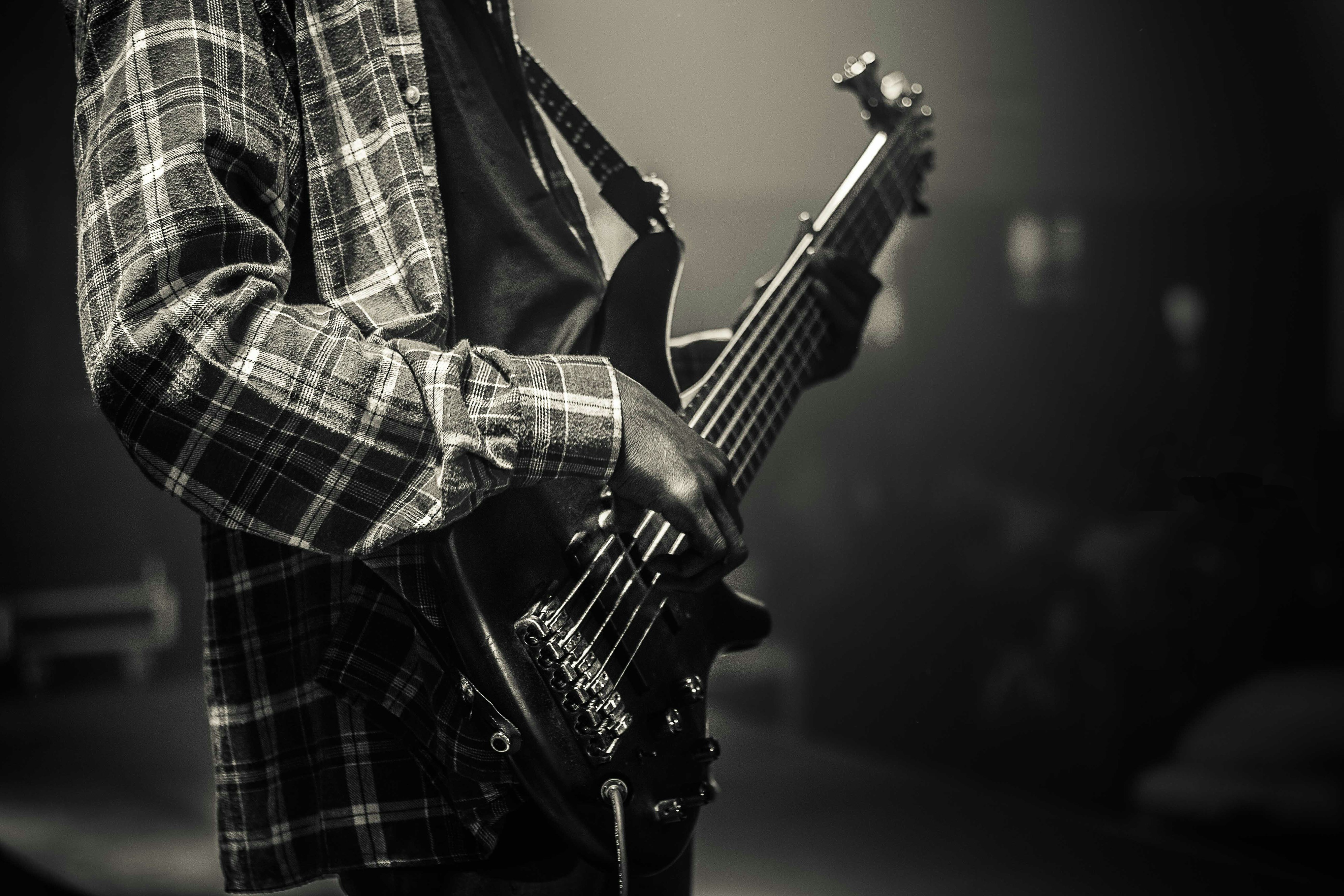 Musician playing an electric guitar on a dimly lit stage, wearing a plaid shirt.